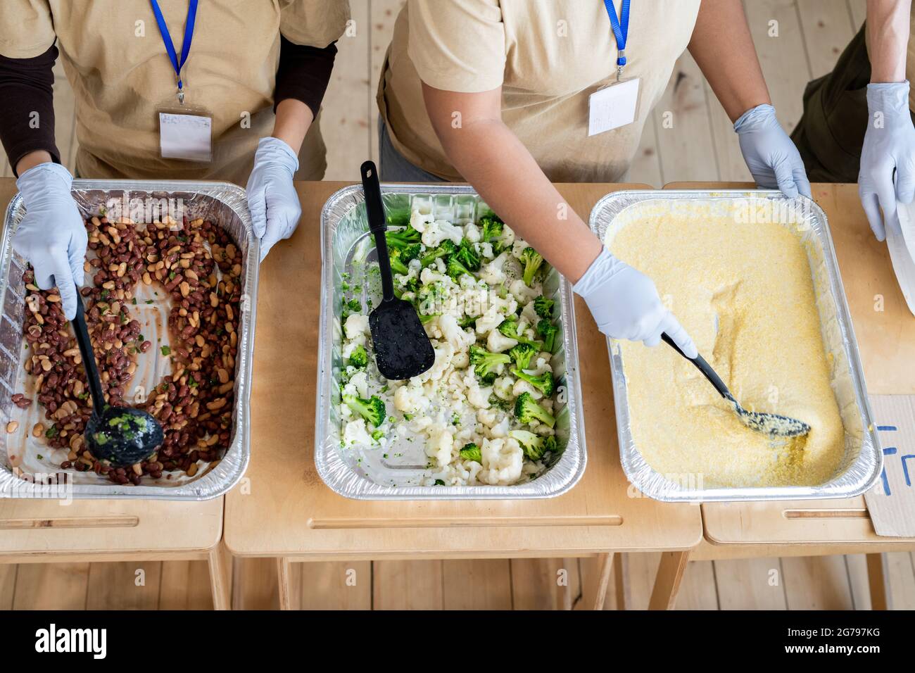 Gloved females standing by table with cooked free food in containers ...