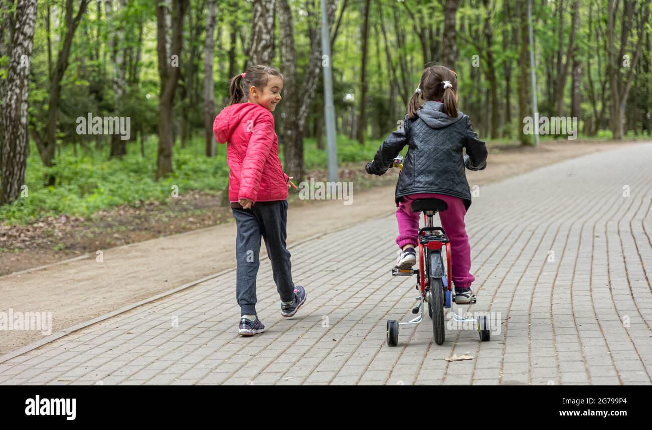 Two little girls ride a bike in the park in spring Stock Photo - Alamy