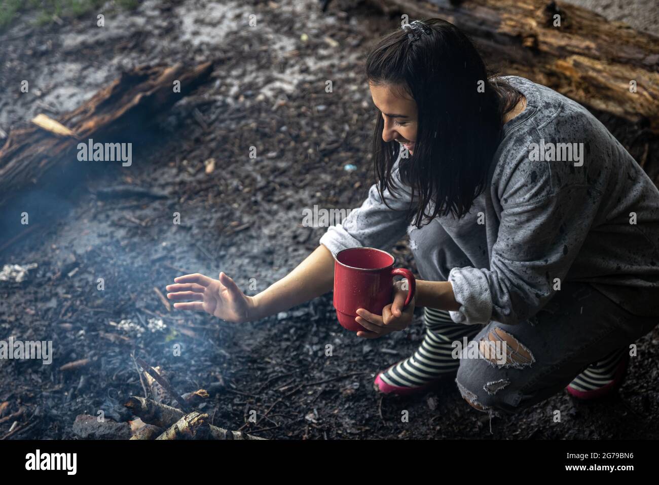A girl with a cup in her hand is fanning the fire to keep warm Stock ...