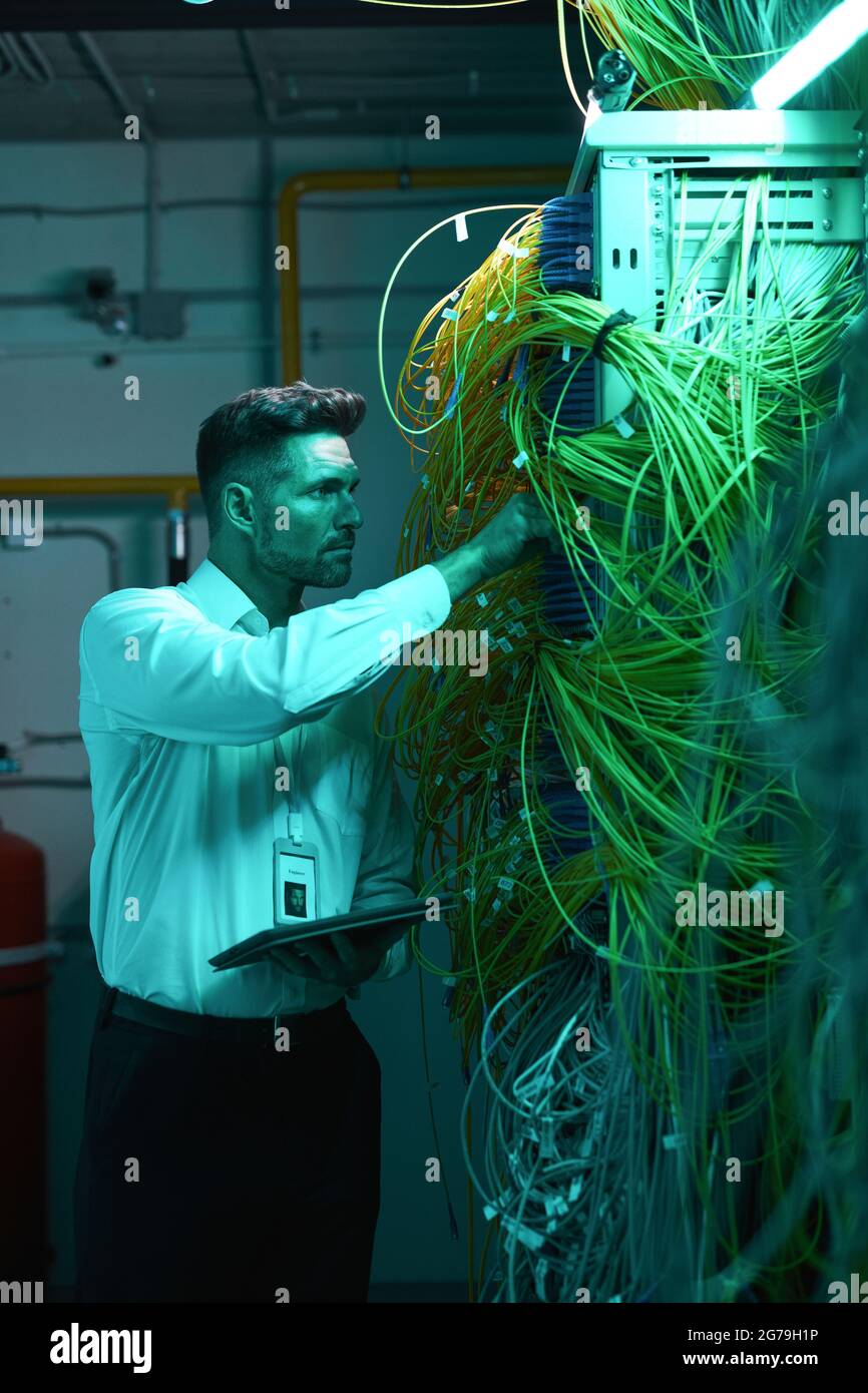 Vertical portrait of handsome data engineer inspecting cables in server ...