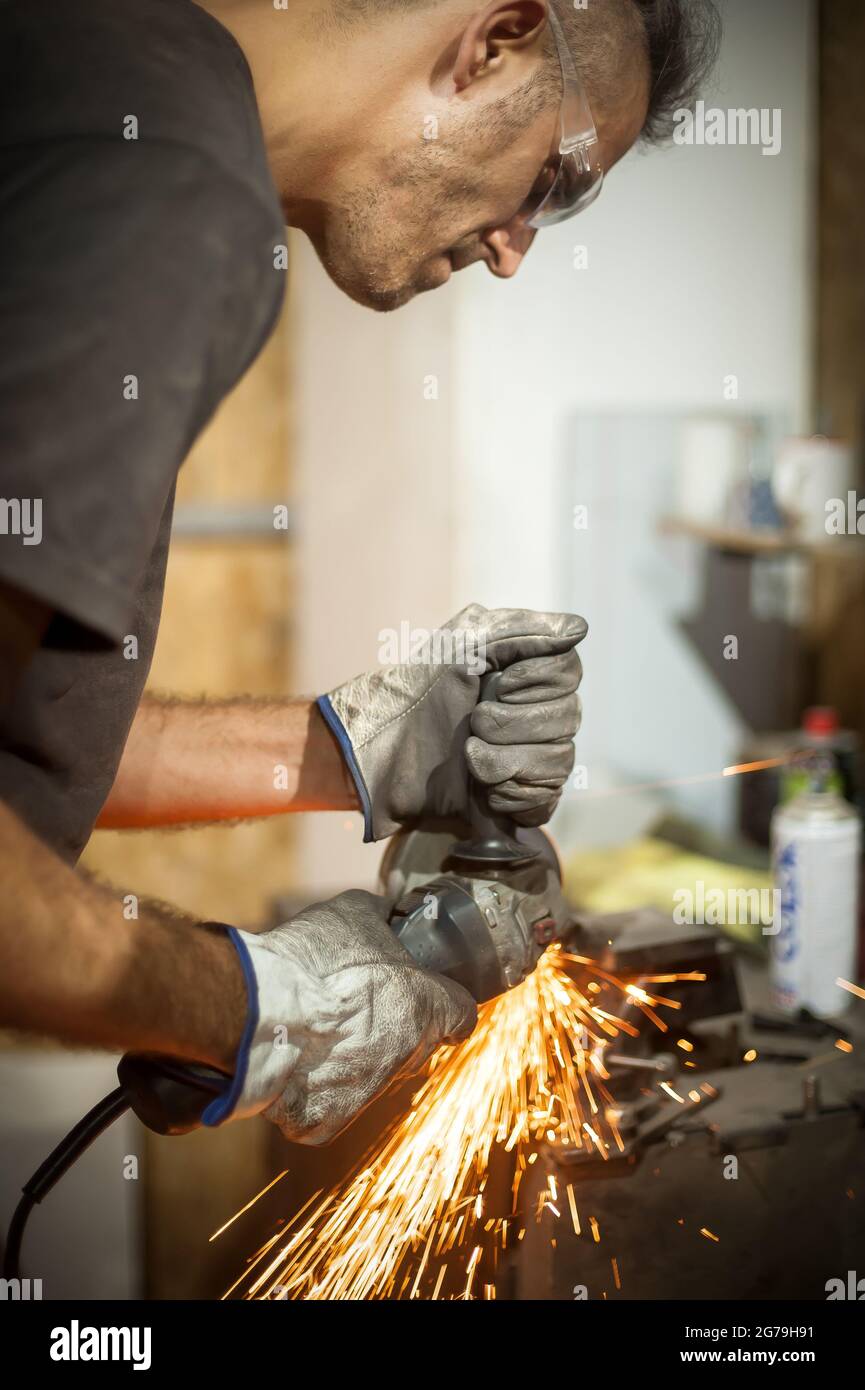 Man working with electric grinder tool on steel structure in factory ...