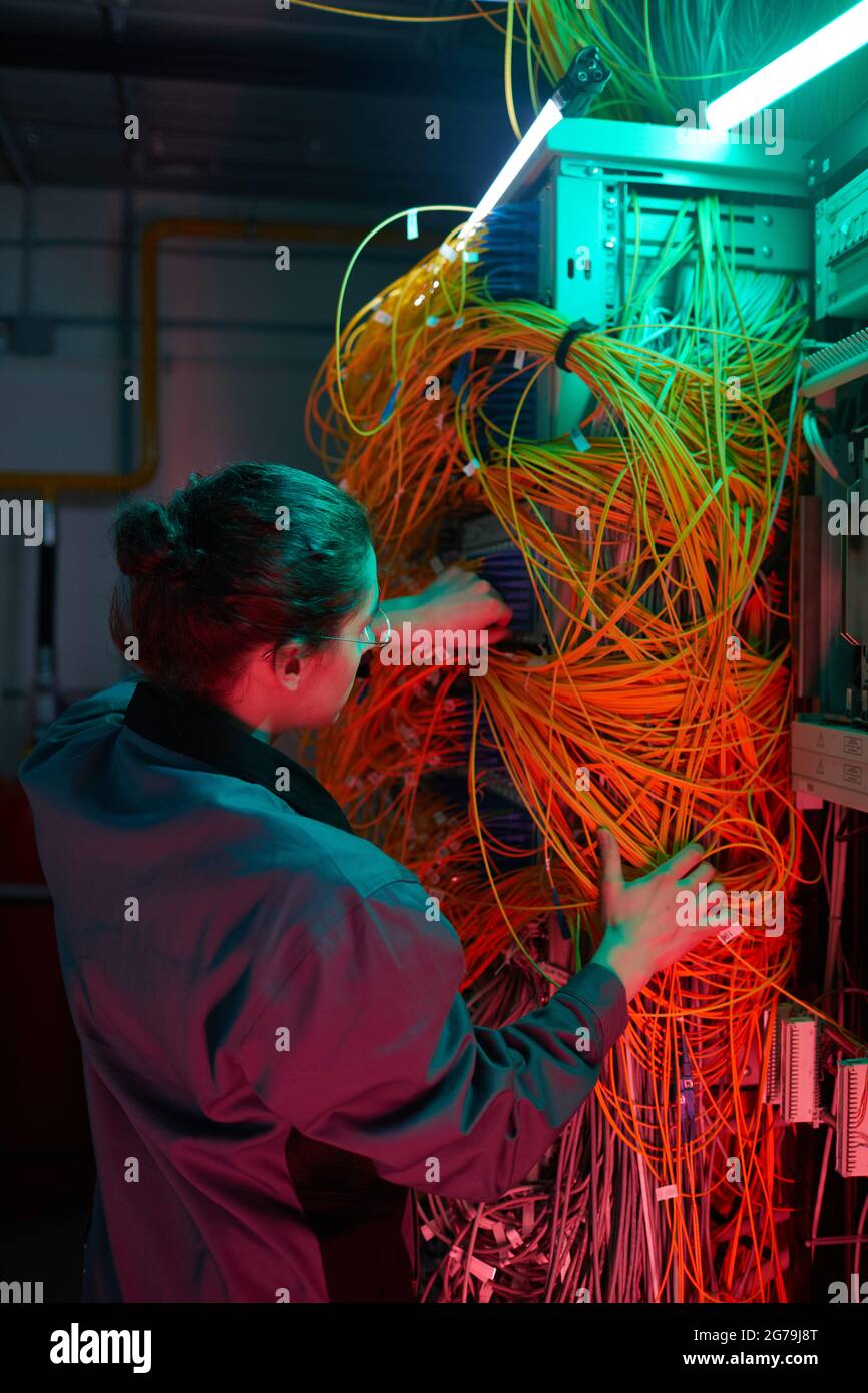 Vertical back view at network technician arranging cables and wires in ...