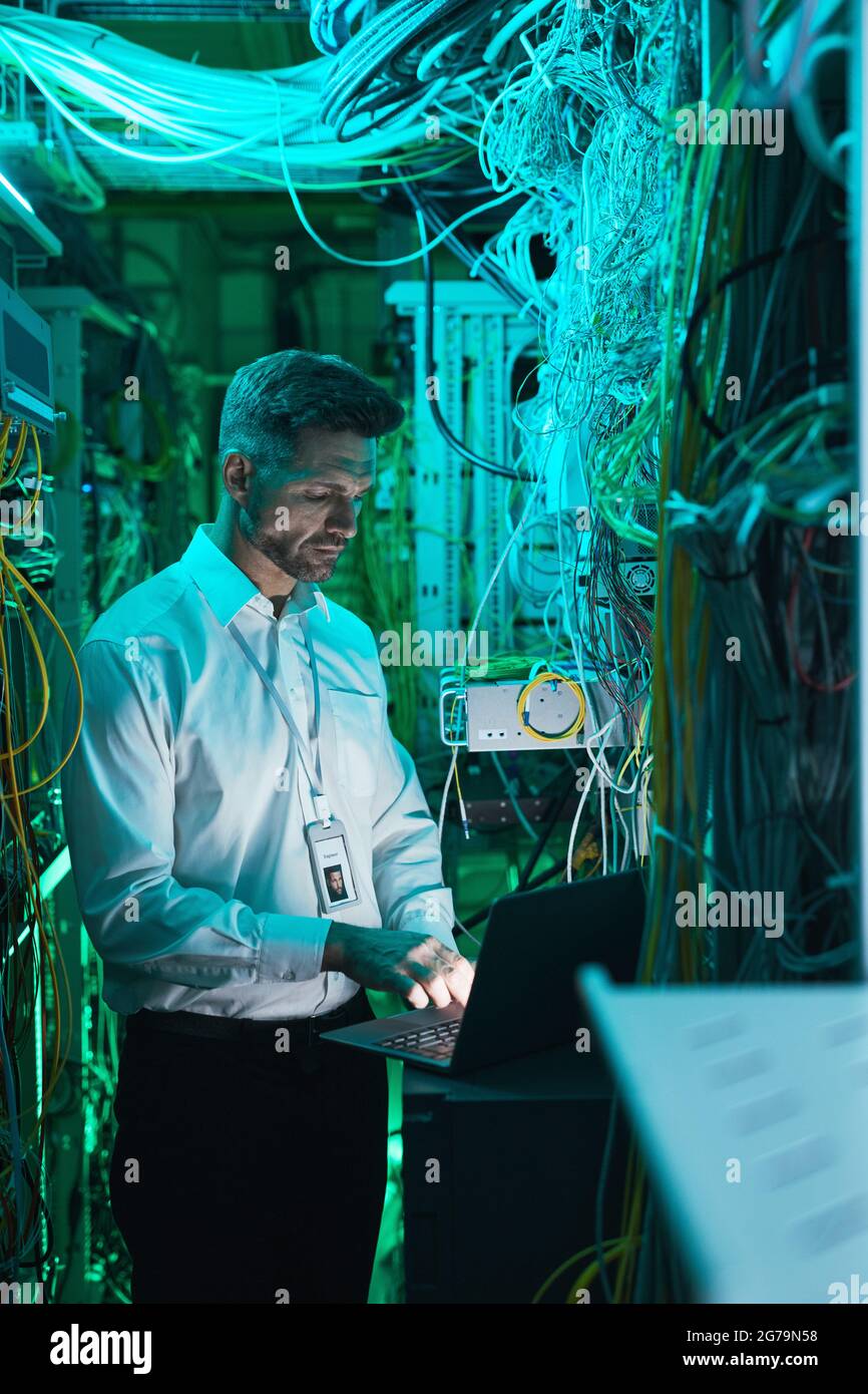 Vertical portrait of mature network technician using laptop in server ...