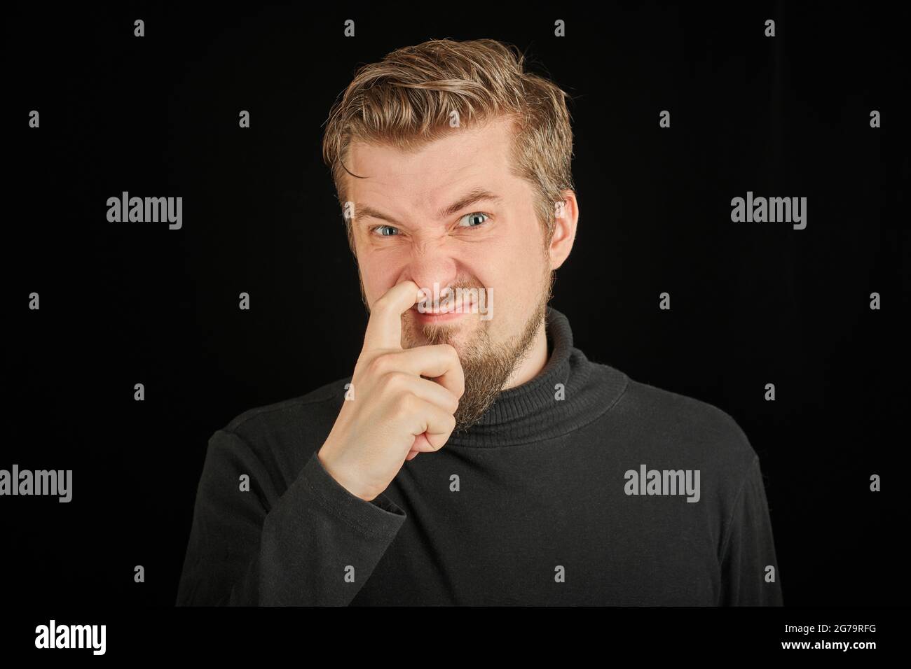 Funny bearded man picking his nose, black background. Young guy in ...