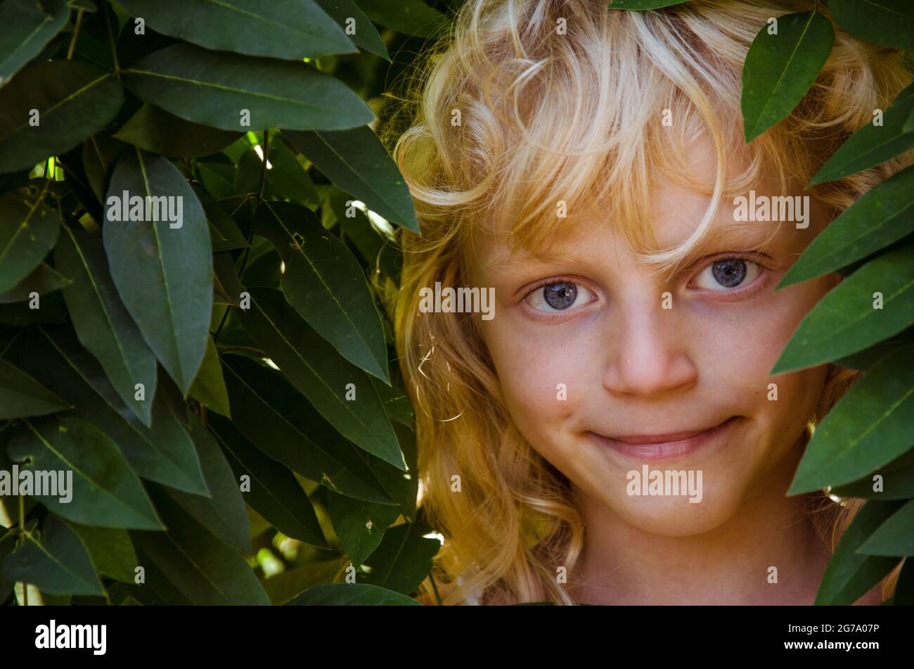 Portrait Of Adorable Girl With Big Blue Eyes Among Green Leaves Stock