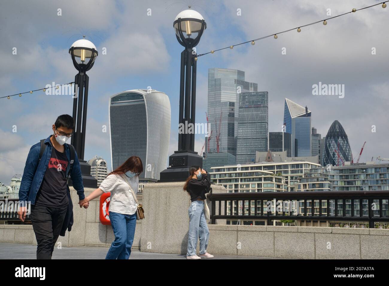 People wearing facemasks walk past a view of the London's skyline, at ...