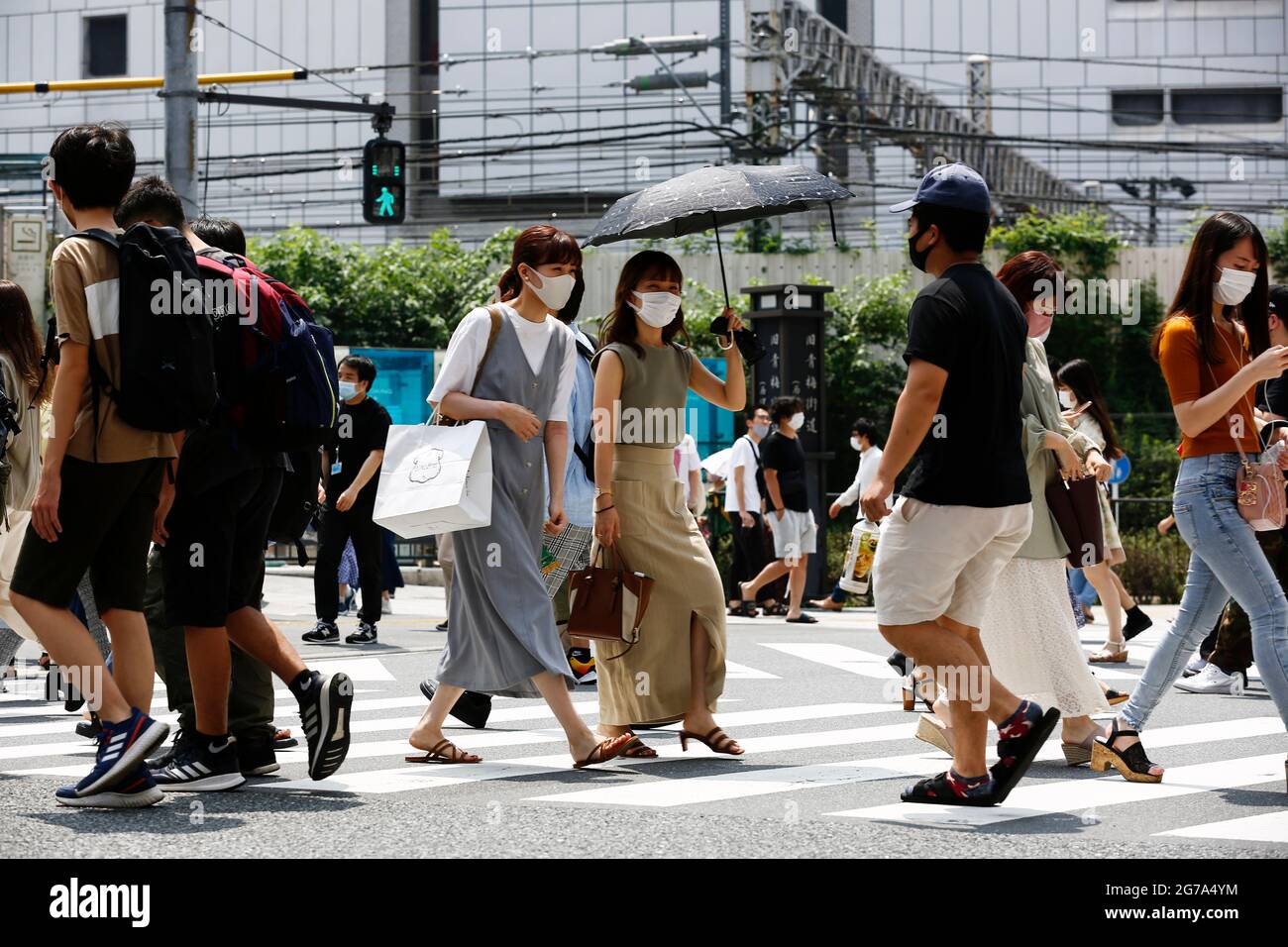 A woman wearing a face mask uses a parasol for shade in the heat in ...