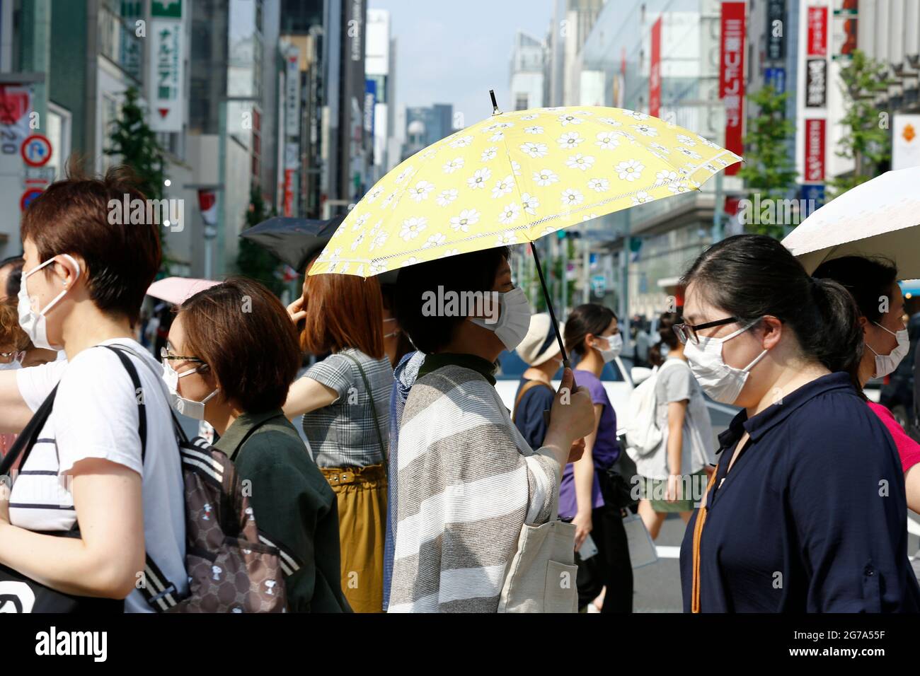 A woman wearing a face mask uses a parasol for shade in the heat at ...