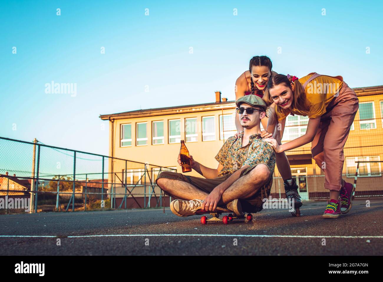 Group of friends hanging out outside. Two girls push their male friend ...