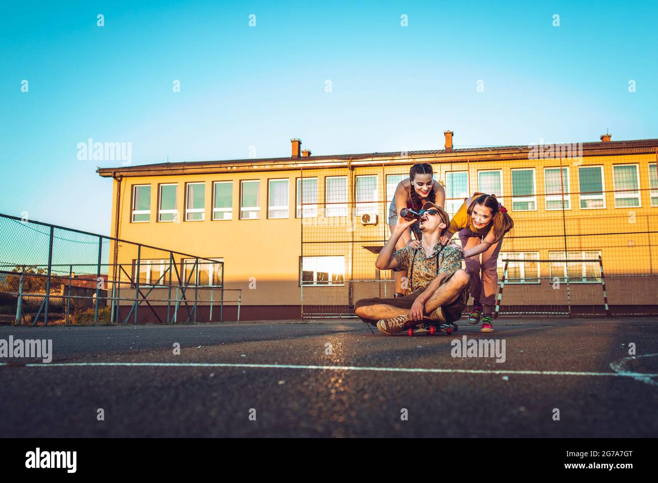 Group of friends hanging out outside. Two girls push their male friend ...