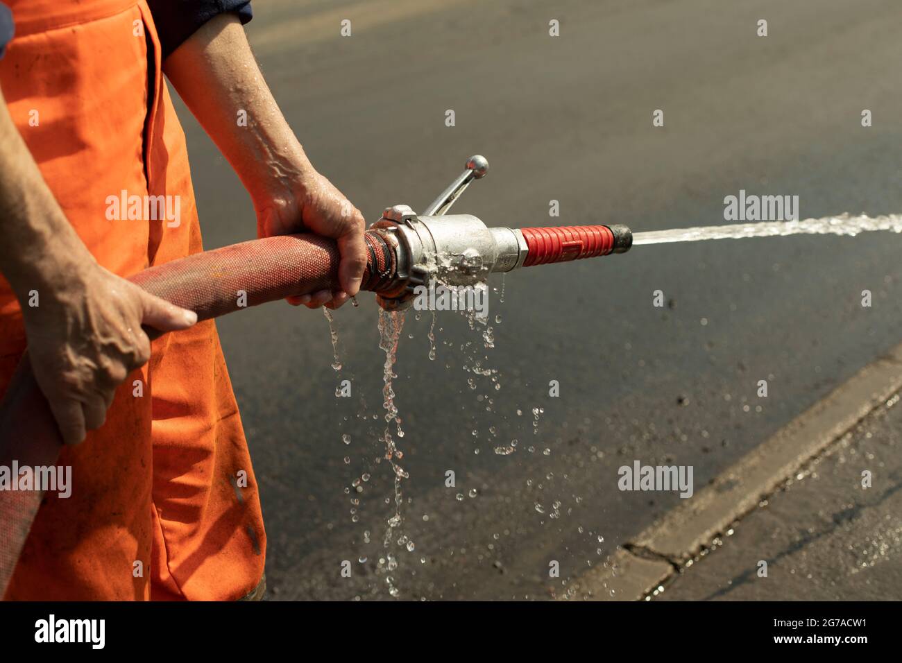 A worker washes the road with a hydrant. Hose with water jet. Washing ...