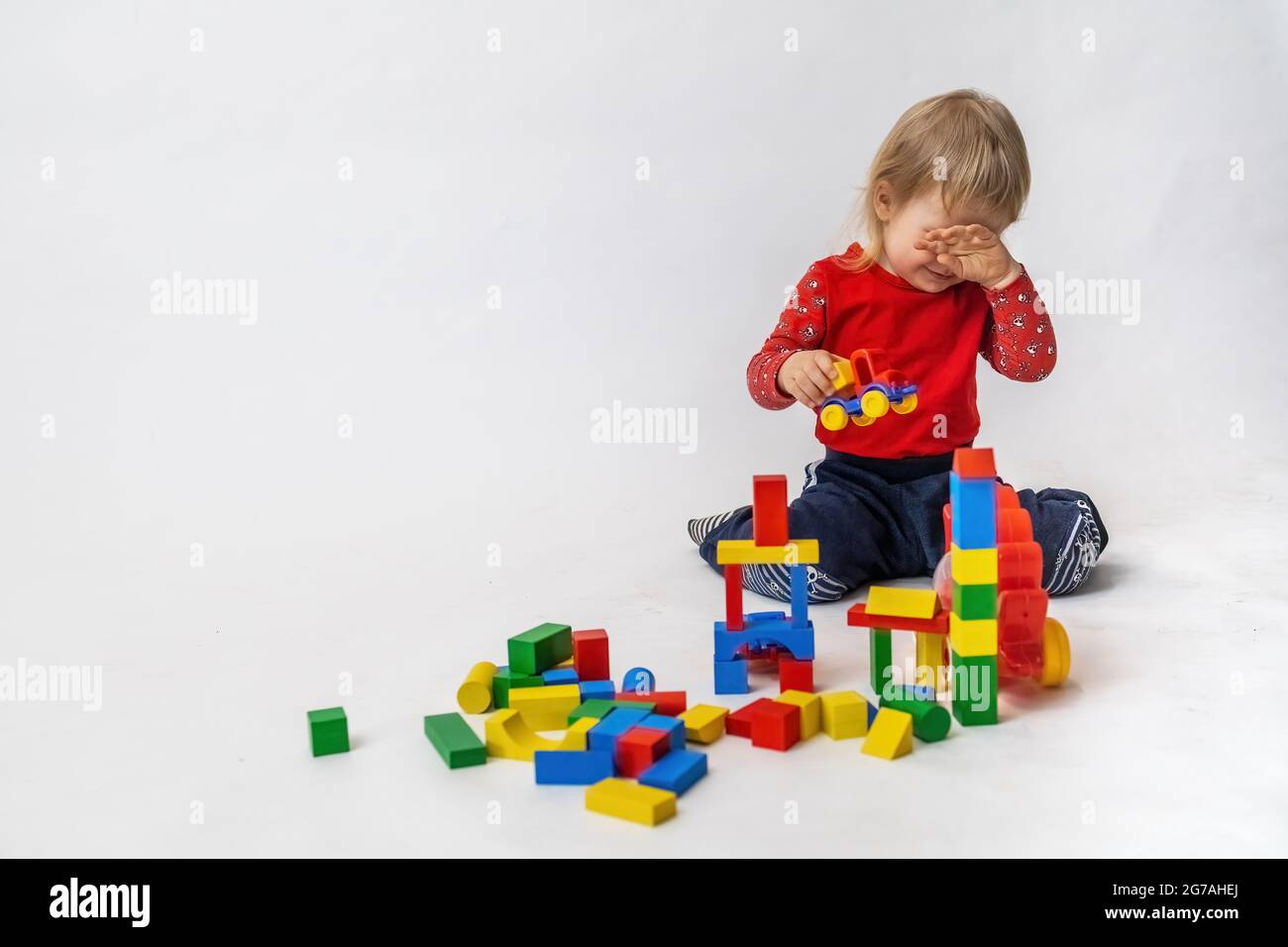 Crying little boy is playing with colorful wooden cubes sitting on the ...