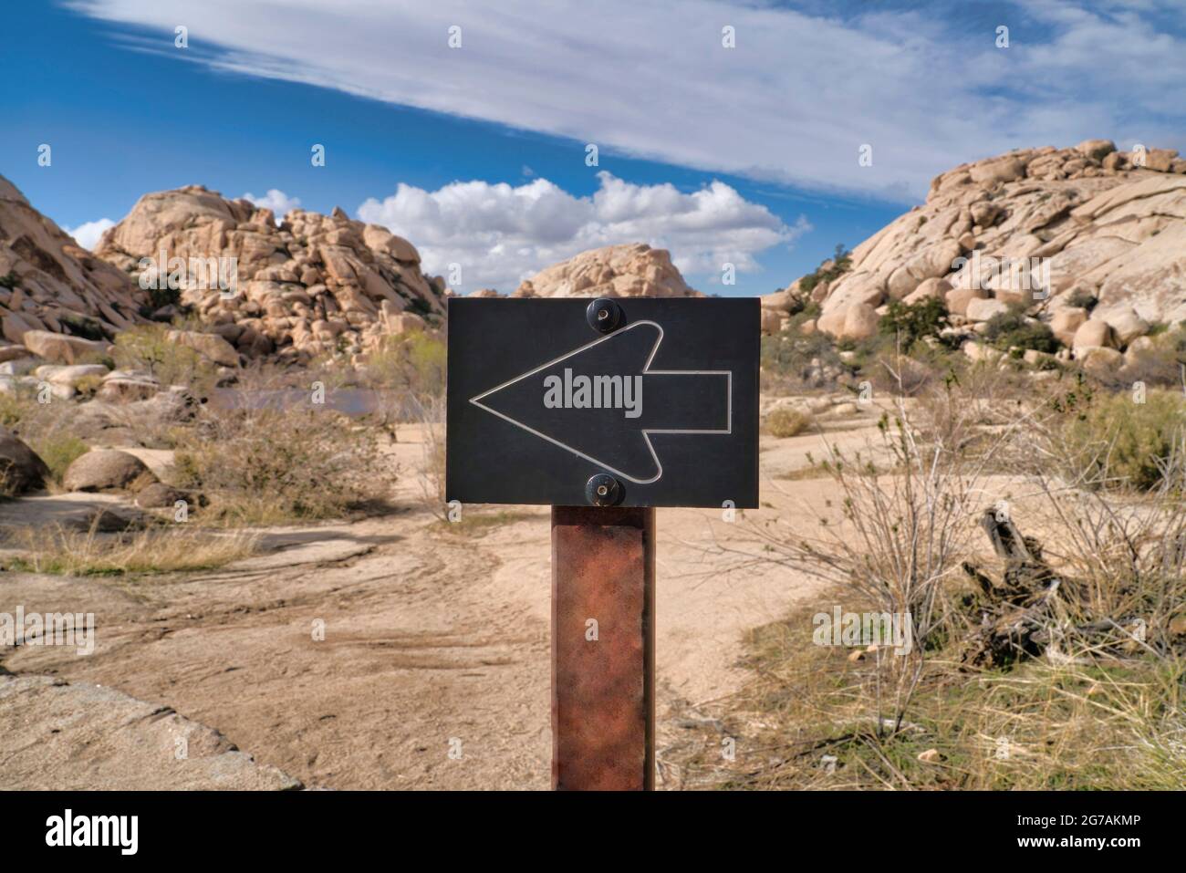Arrow directional sign against rocks and blue sky at Joshua Tree ...