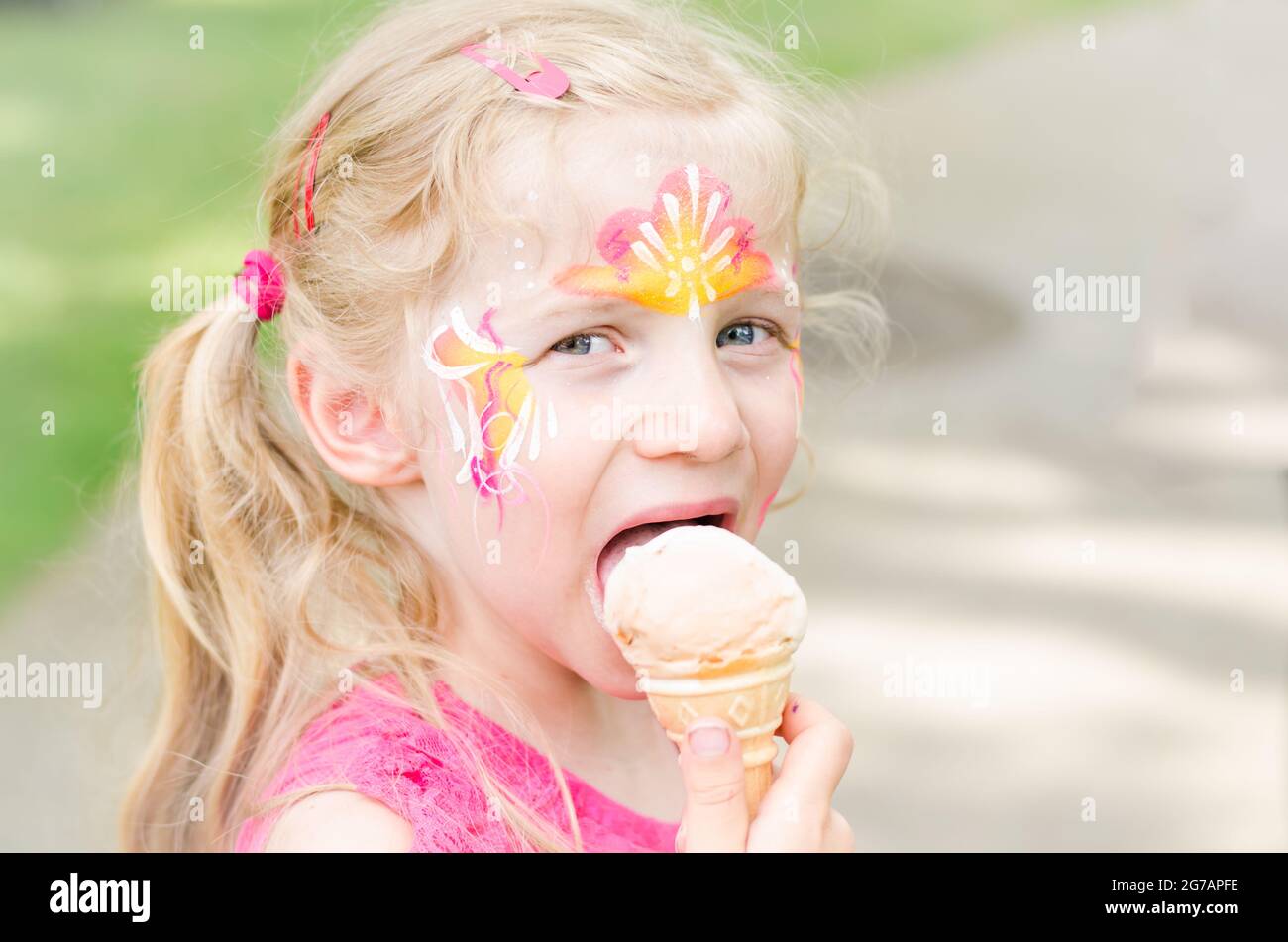 little lovely blond girl with colorful facepainting with ice cream ...
