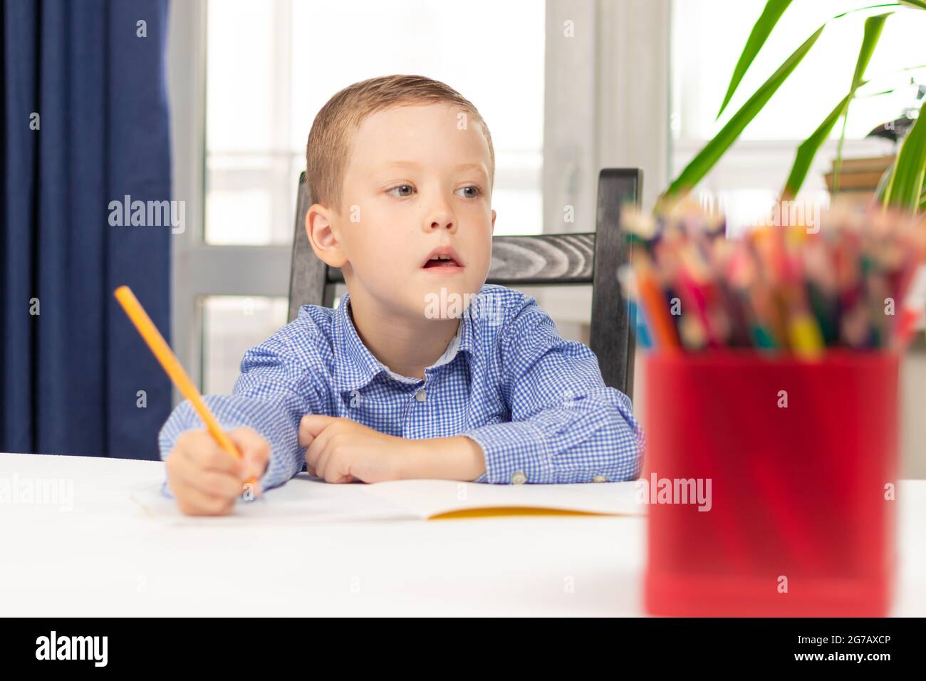 Cute seven year old child boy doing homework at home on a white wooden ...