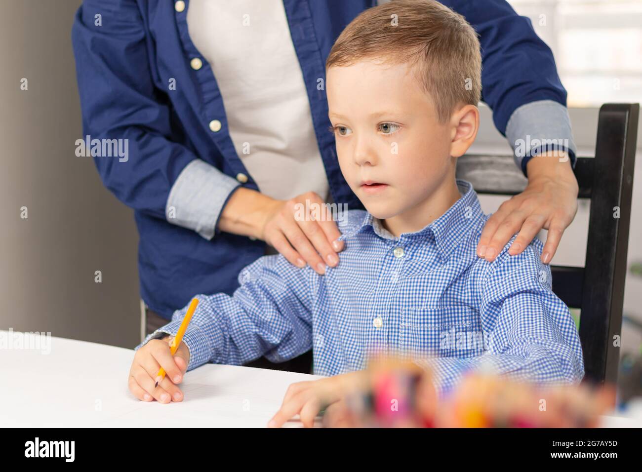 Cute seven year old baby boy doing homework at home with mom on a white ...