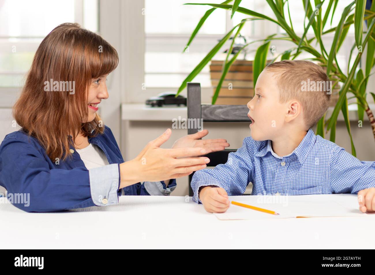Cute seven year old baby boy doing homework at home with mom on a white ...
