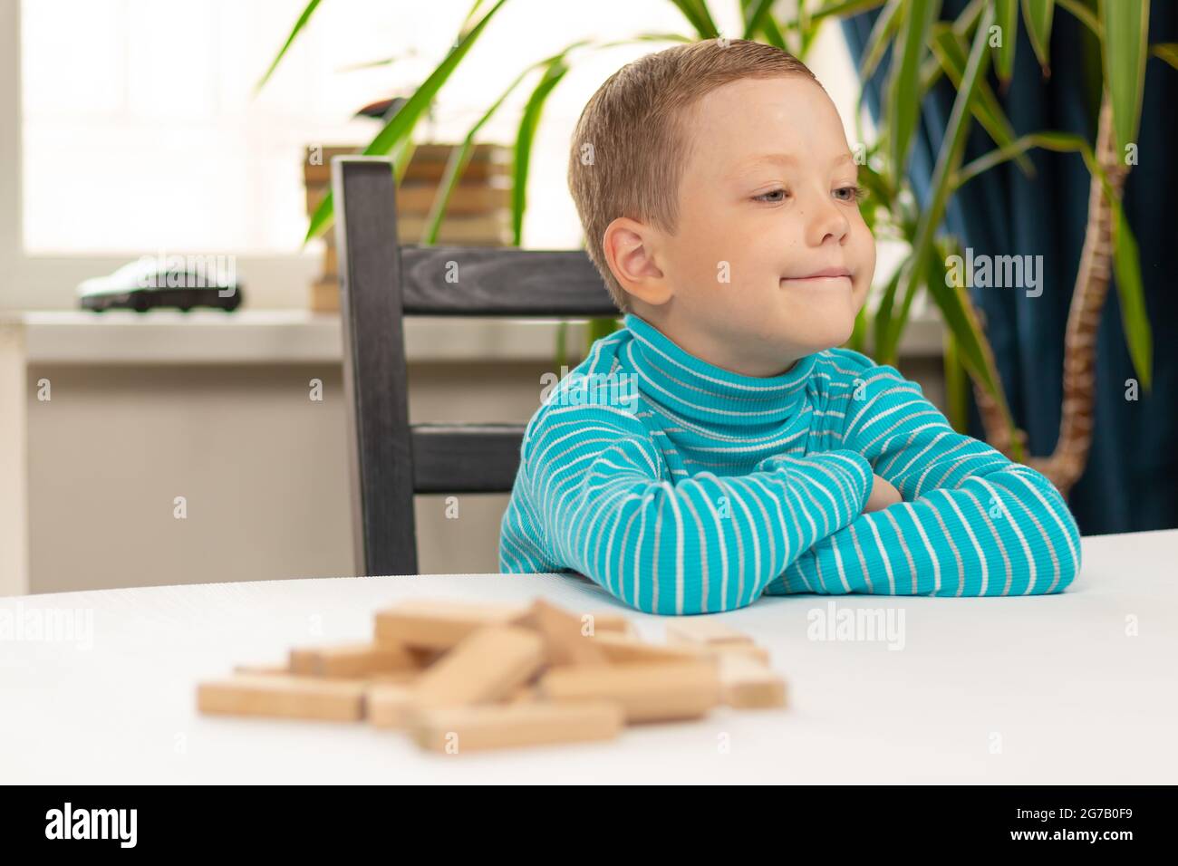 A cute seven-year-old child boy playing Jenga at home at a white wooden ...