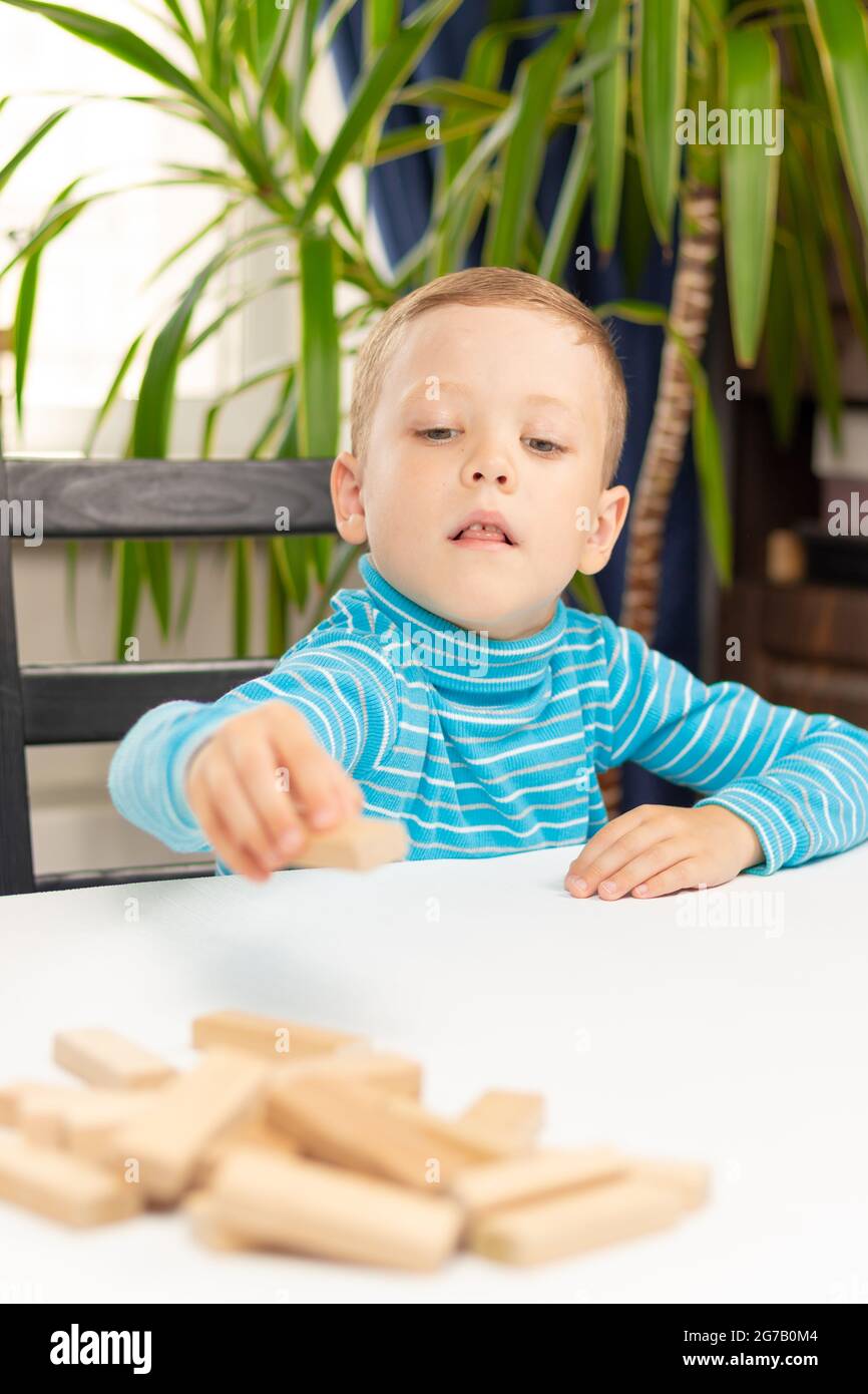 A cute seven-year-old child boy playing Jenga at home at a white wooden ...