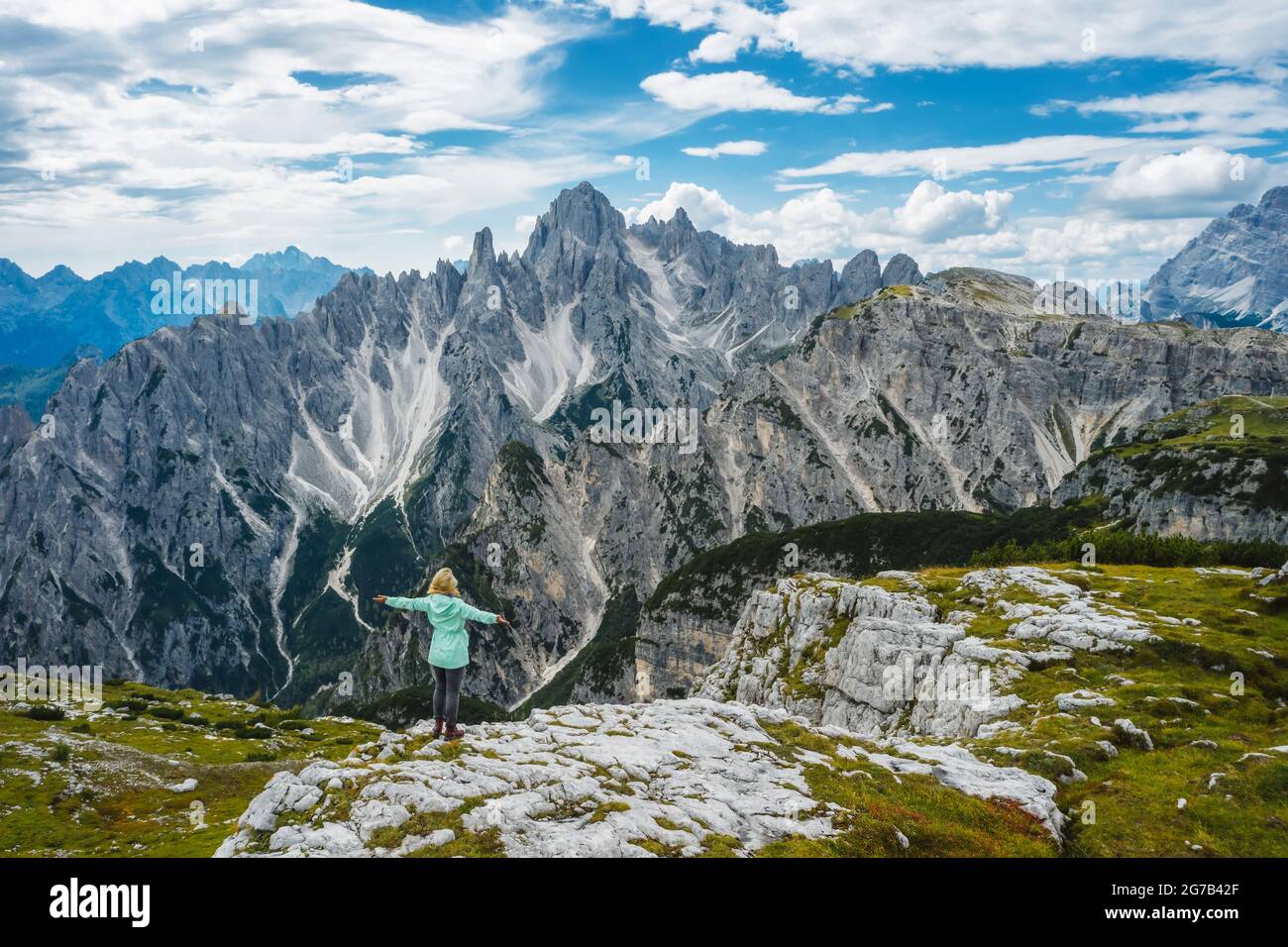 Aerial view of a woman hiker in green jacket with raised hands admiring ...