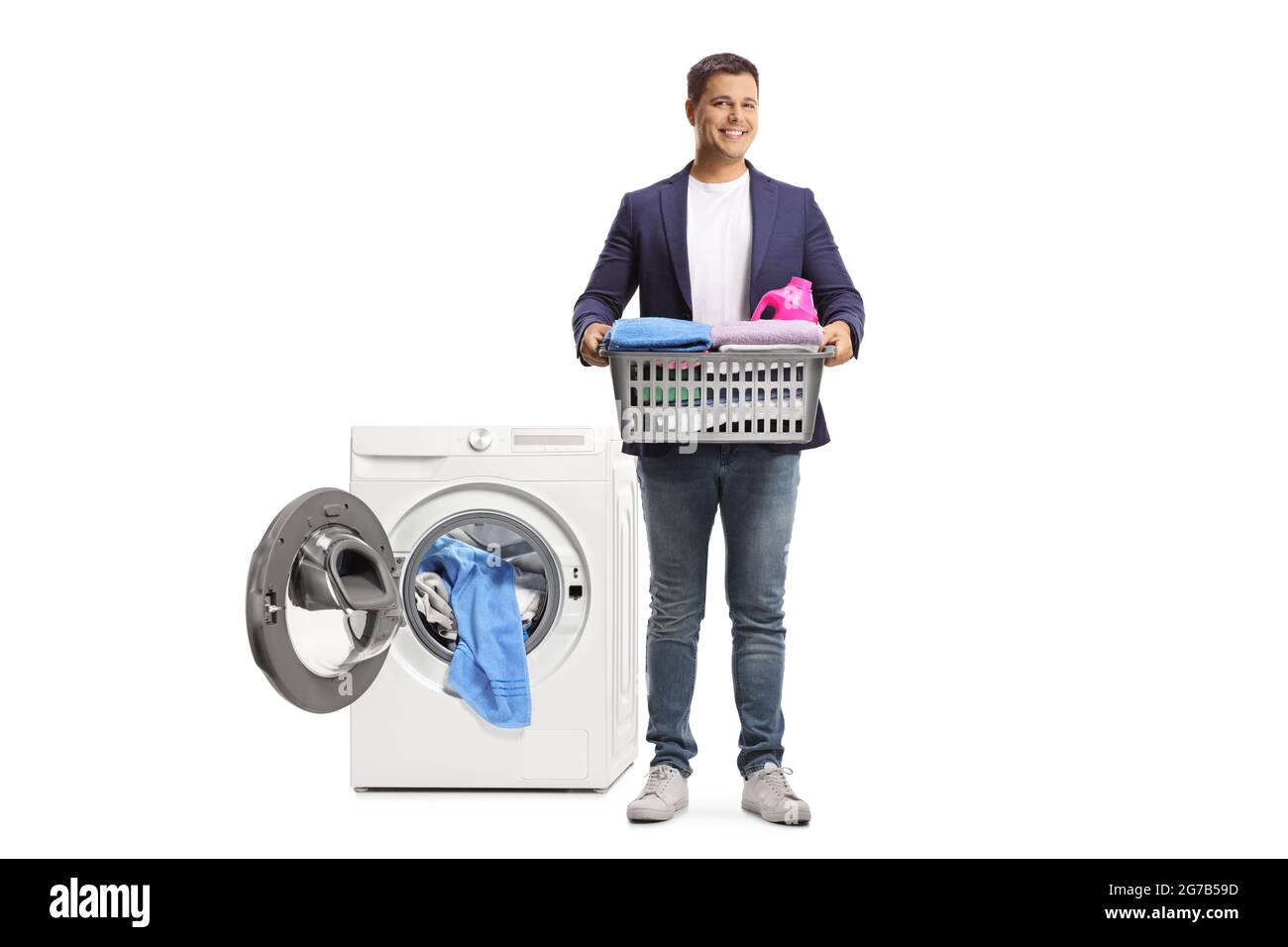 Young man carrying a laundry basket with clothes in front of a washing ...