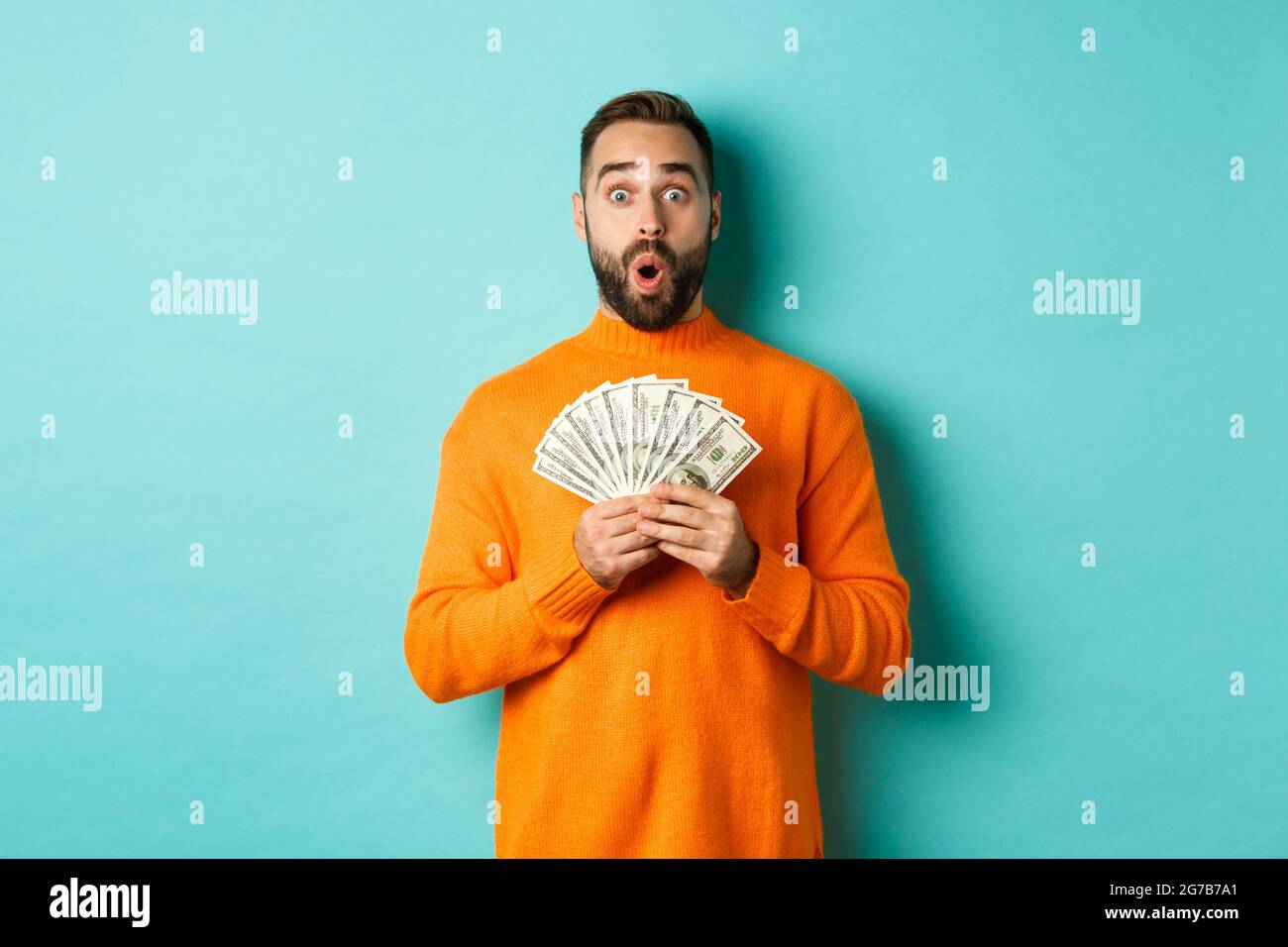 Photo of surprised guy holding money, looking amazed, standing with ...