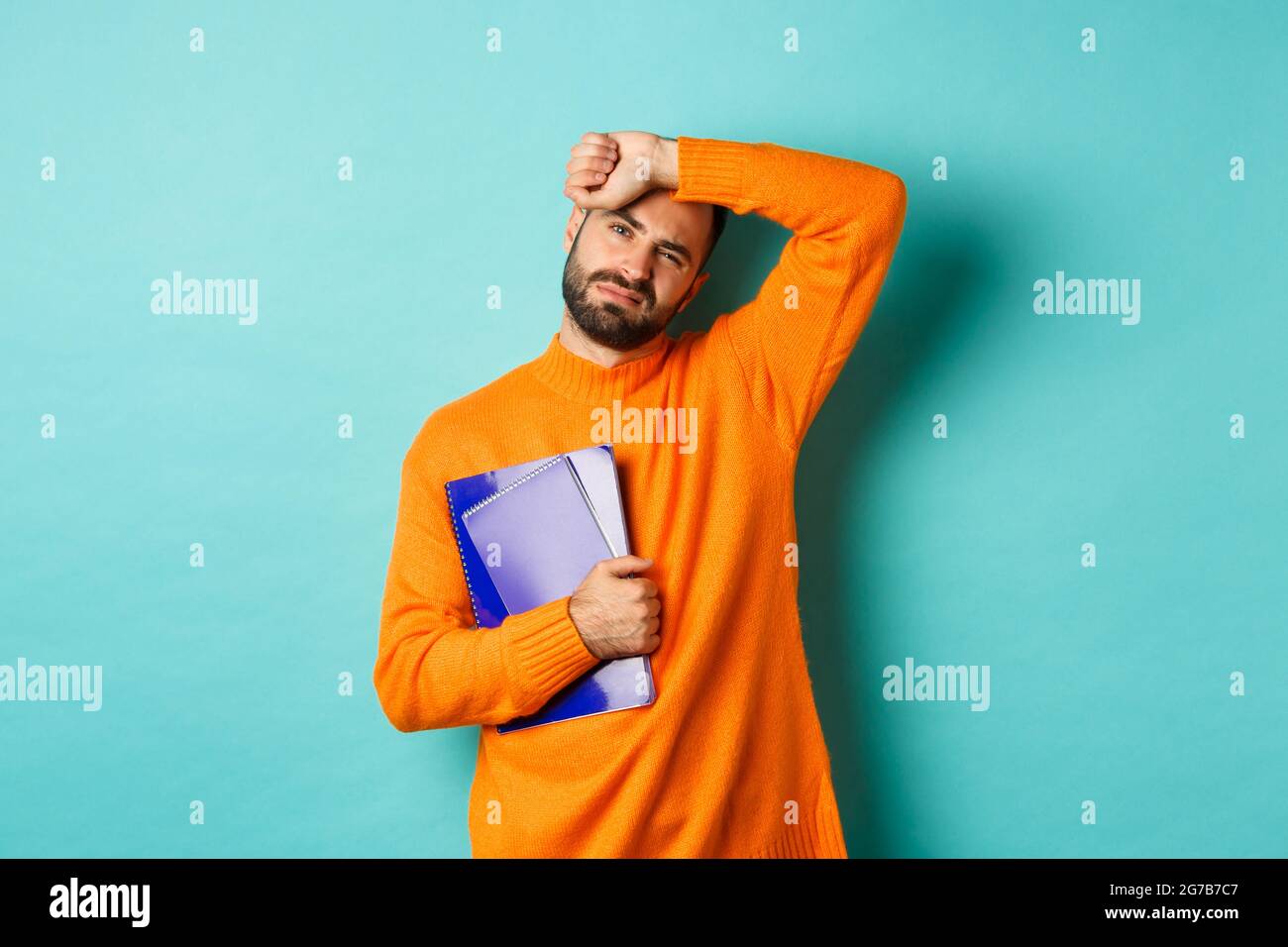 Education. Tired male student holding notebooks and wiping sweat off ...