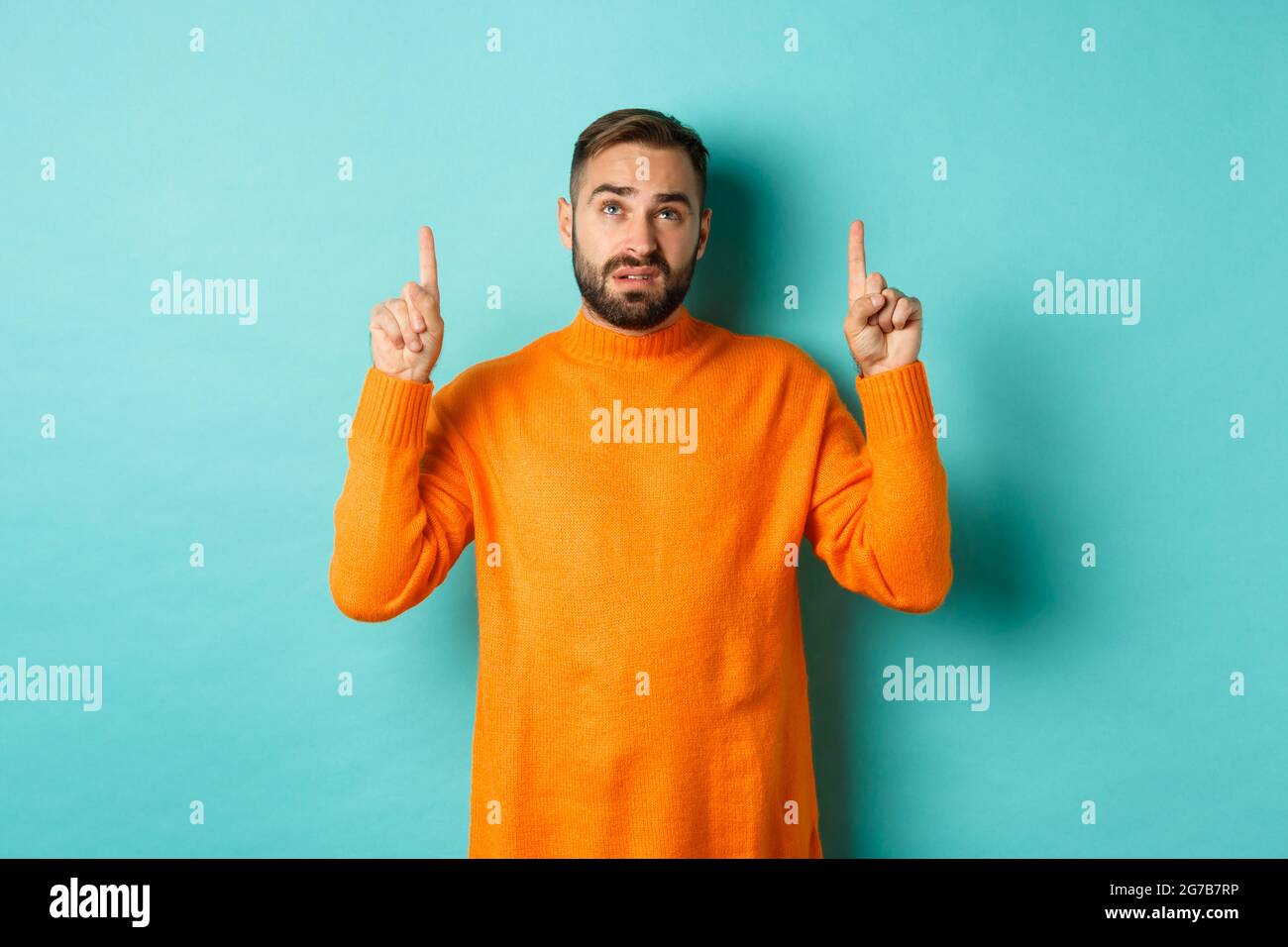 Doubtful and unamused man looking, pointing fingers up something ...