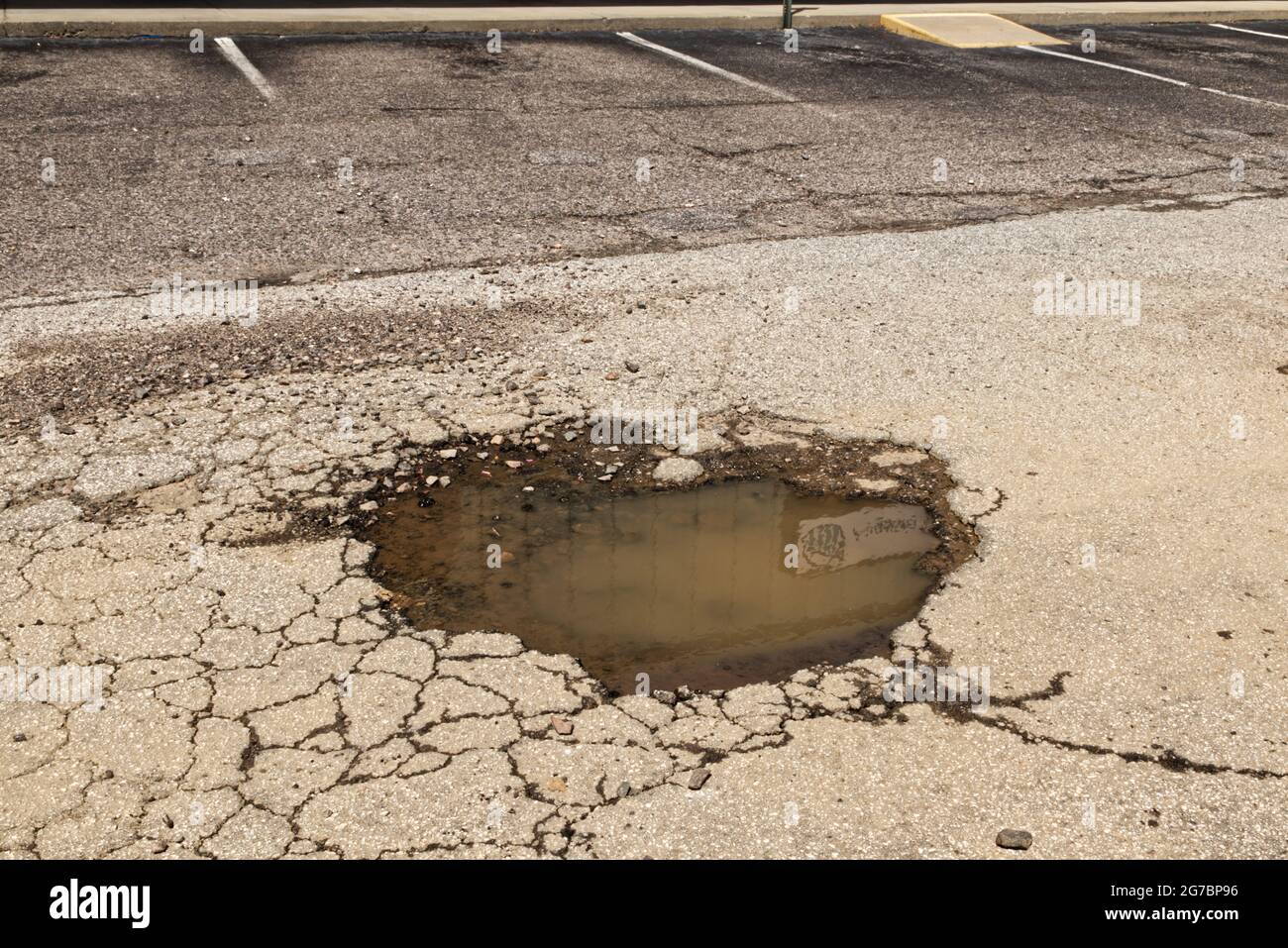 A large pot hole in the road with cracks and filled with water in a lot ...