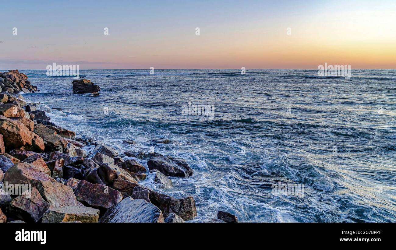 Pano Ocean waves crashing on jagged rocks with blue sky and golden sun ...