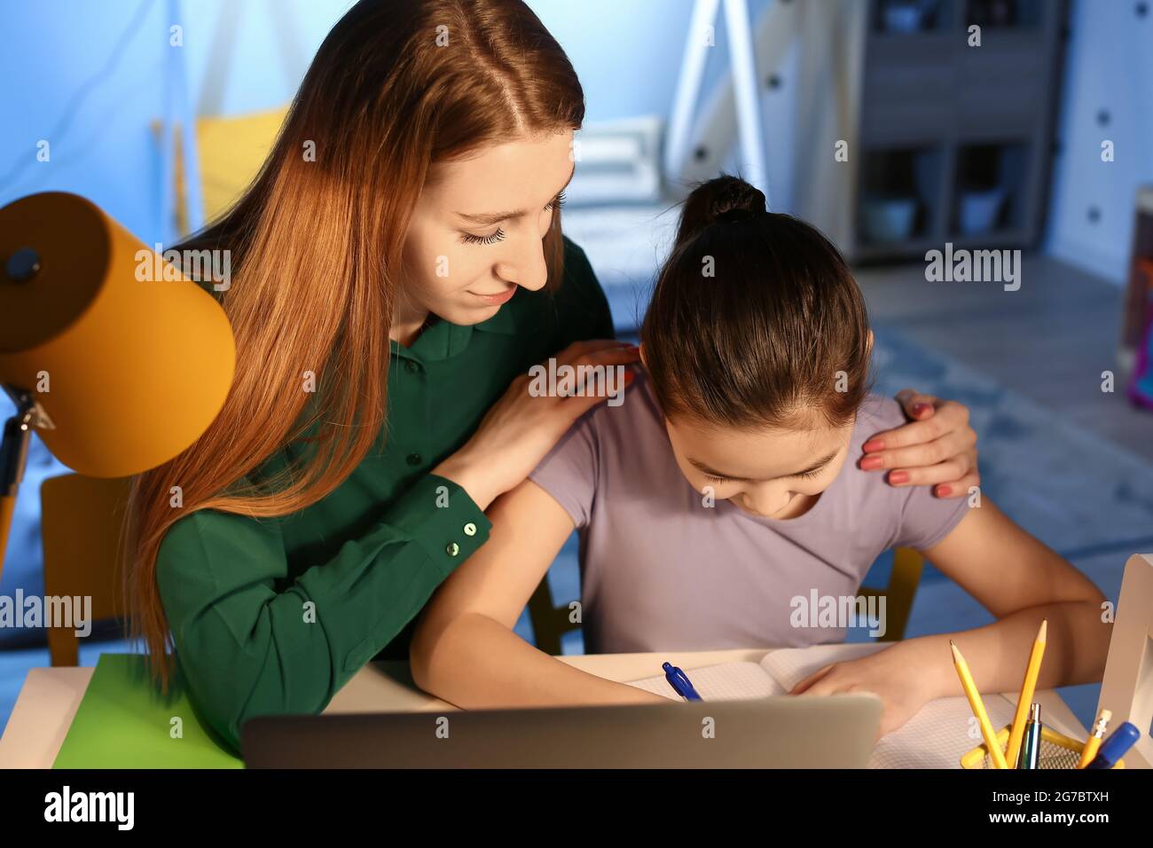 Little girl with her mother doing homework at home late in evening ...