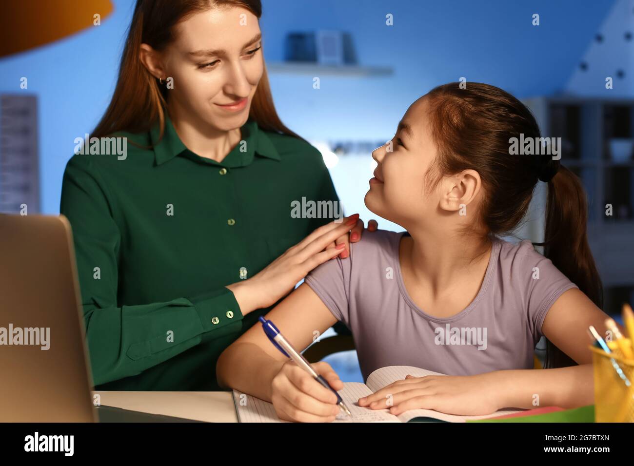 Little girl with her mother doing homework at home late in evening ...