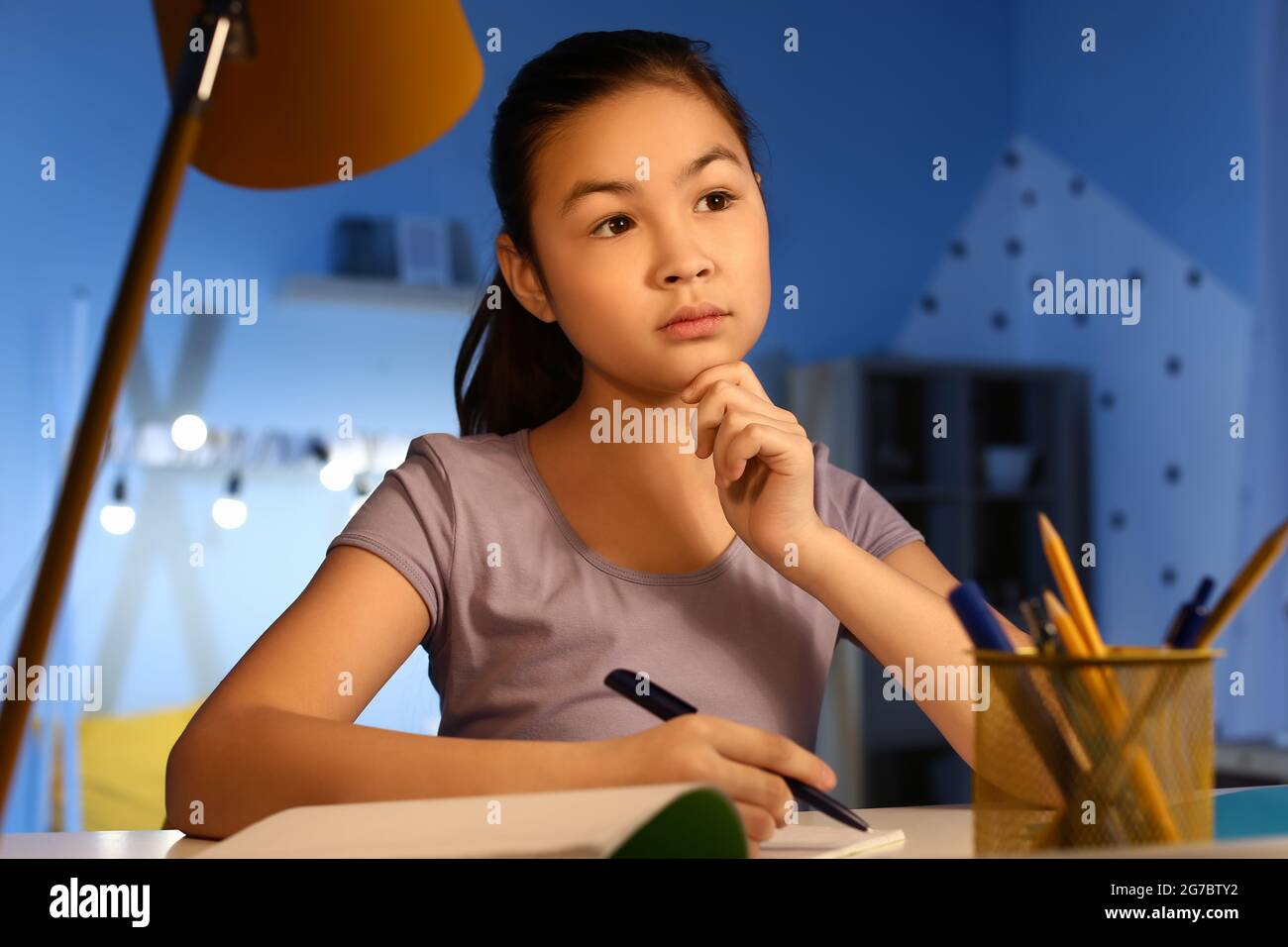 Thoughtful little girl doing homework at home late in evening Stock ...