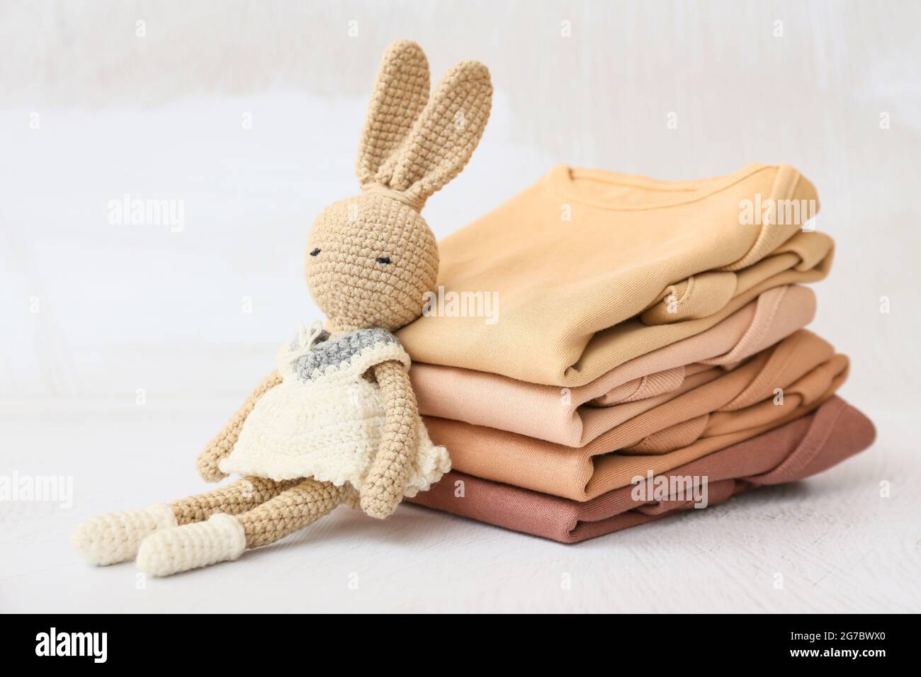 Stack of baby clothes and knitted toy on light background Stock Photo ...