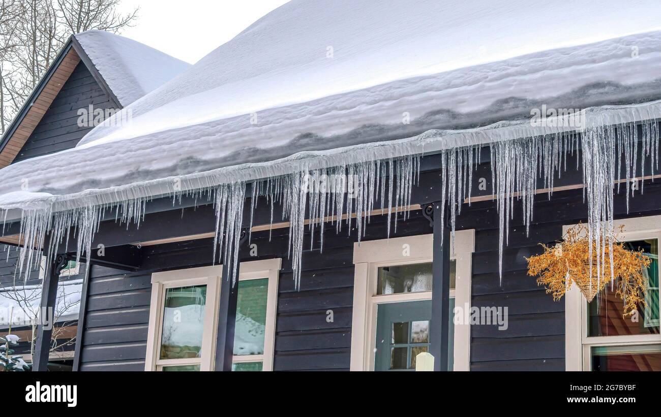 Pano Gabled roof of home covered with thick snow and lined with icicles ...