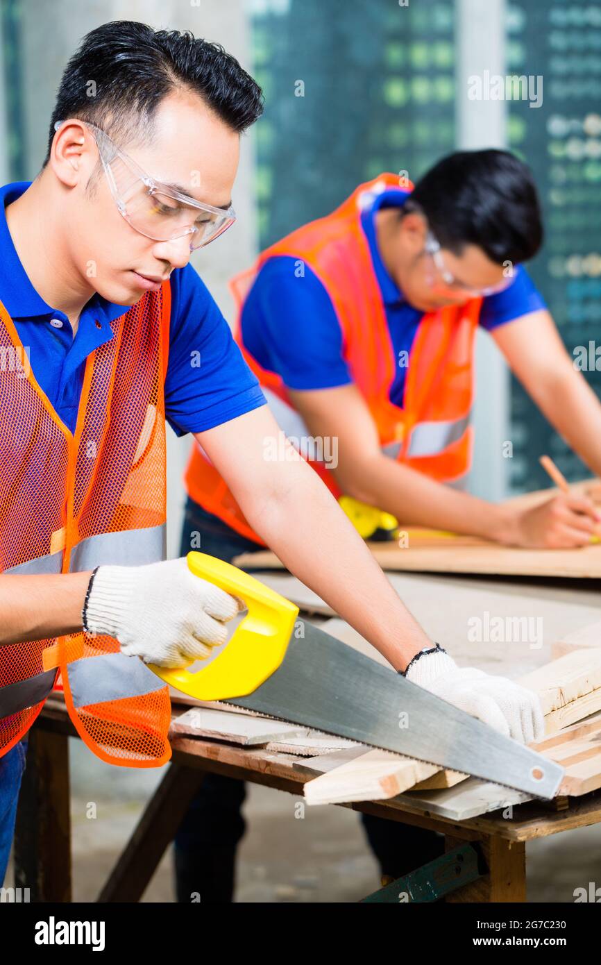 Asian Indonesian builder or craftsman sawing with a saw a wood board of ...