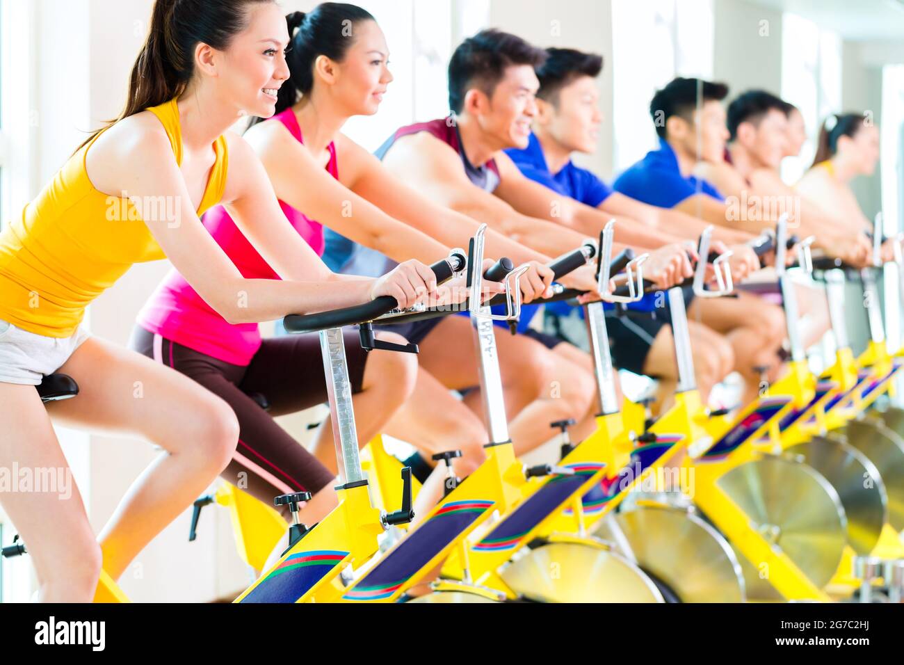Chinese Asian sport group of men and women in fitness club or gym exercising on spinning bikes ...