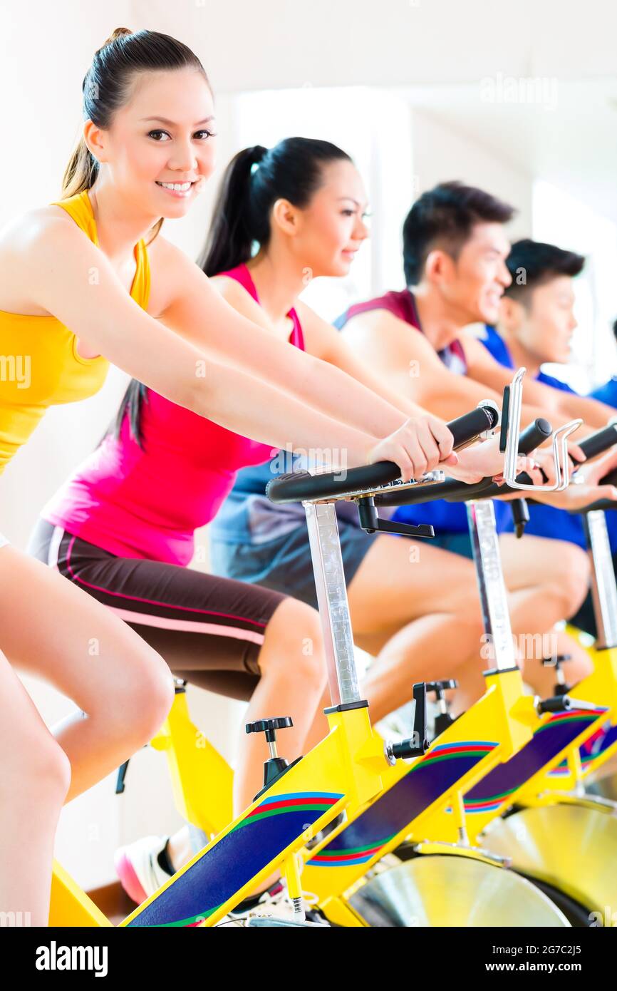 Chinese Asian sport group of men and women in fitness club or gym exercising on spinning bikes ...