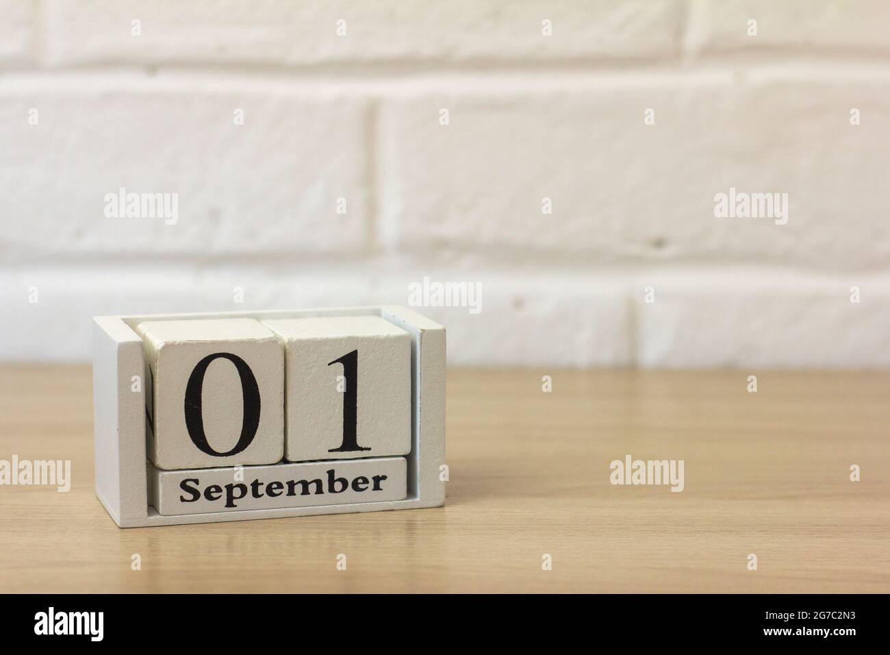 September 1. Wooden calendar on a white brick background with an empty ...