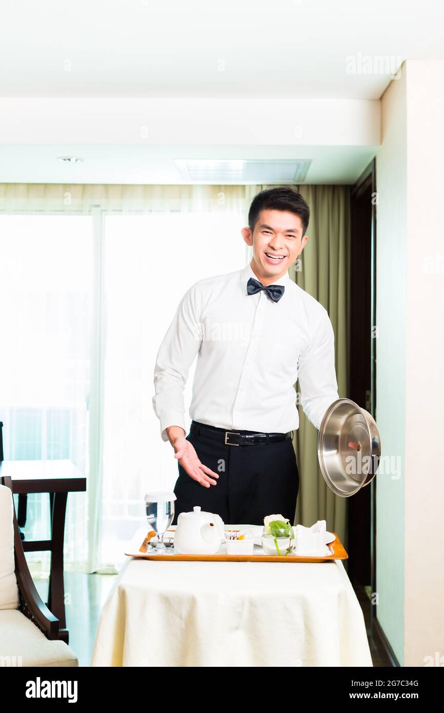Asian Chinese room service waiter or steward serving guests food in a ...