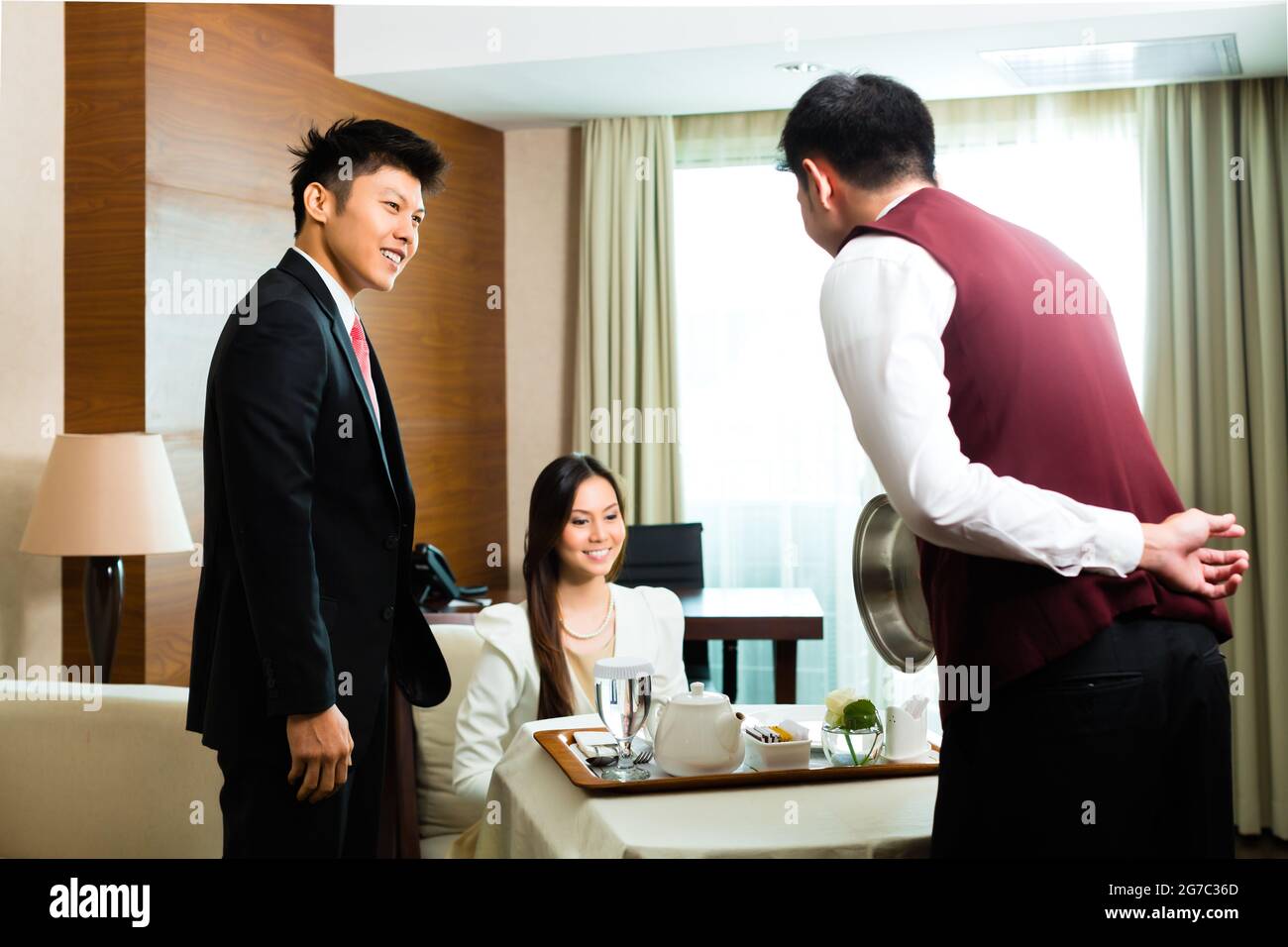 Asian Chinese room service waiter or steward serving guests food in a ...
