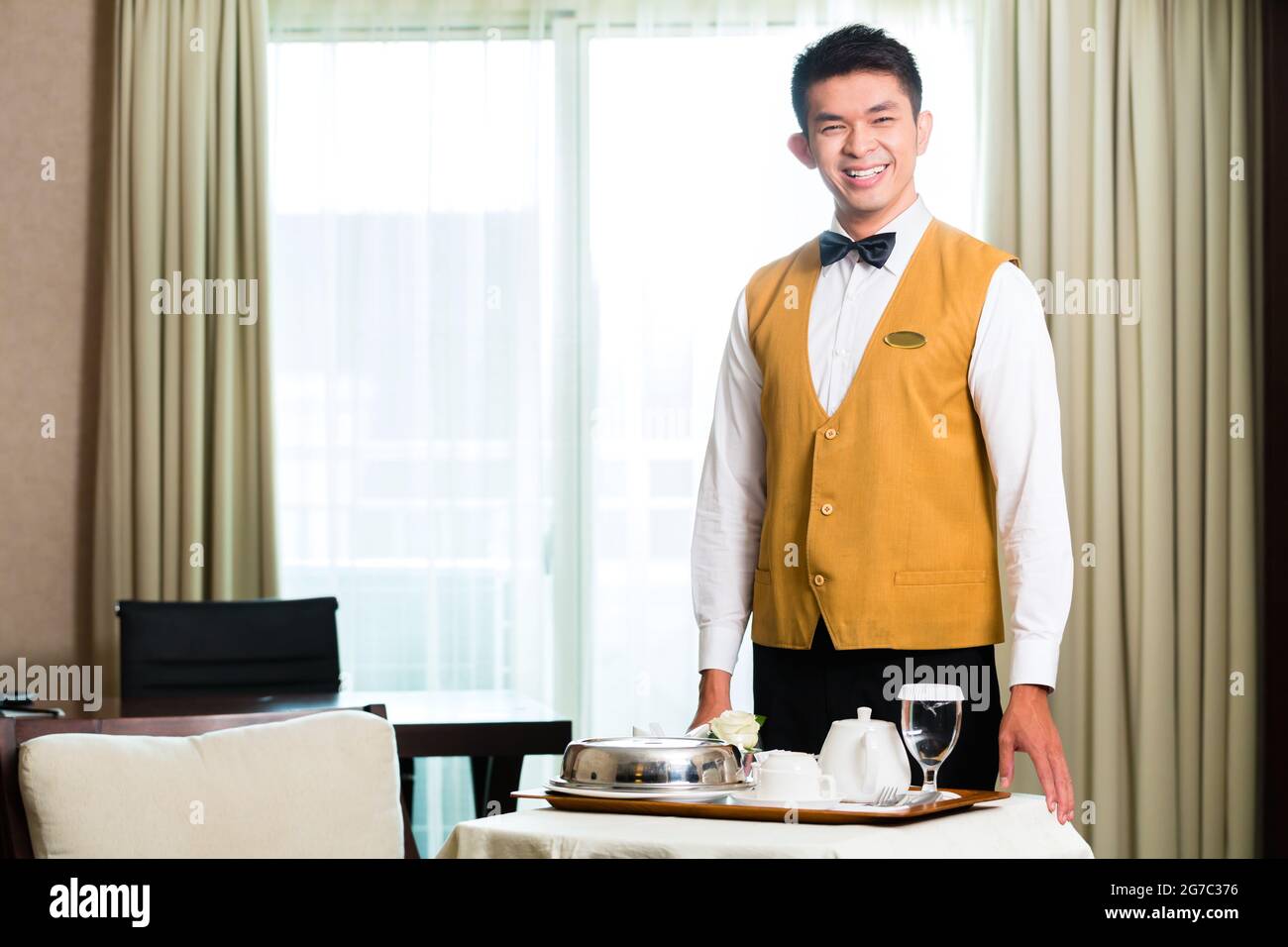 Asian Chinese room service waiter or steward serving guests food in a ...