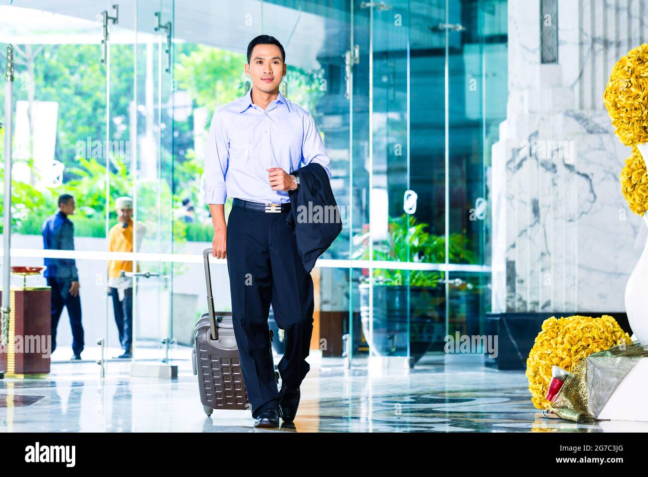 Asian man walking and pulling suitcase in hotel lobby Stock Photo - Alamy