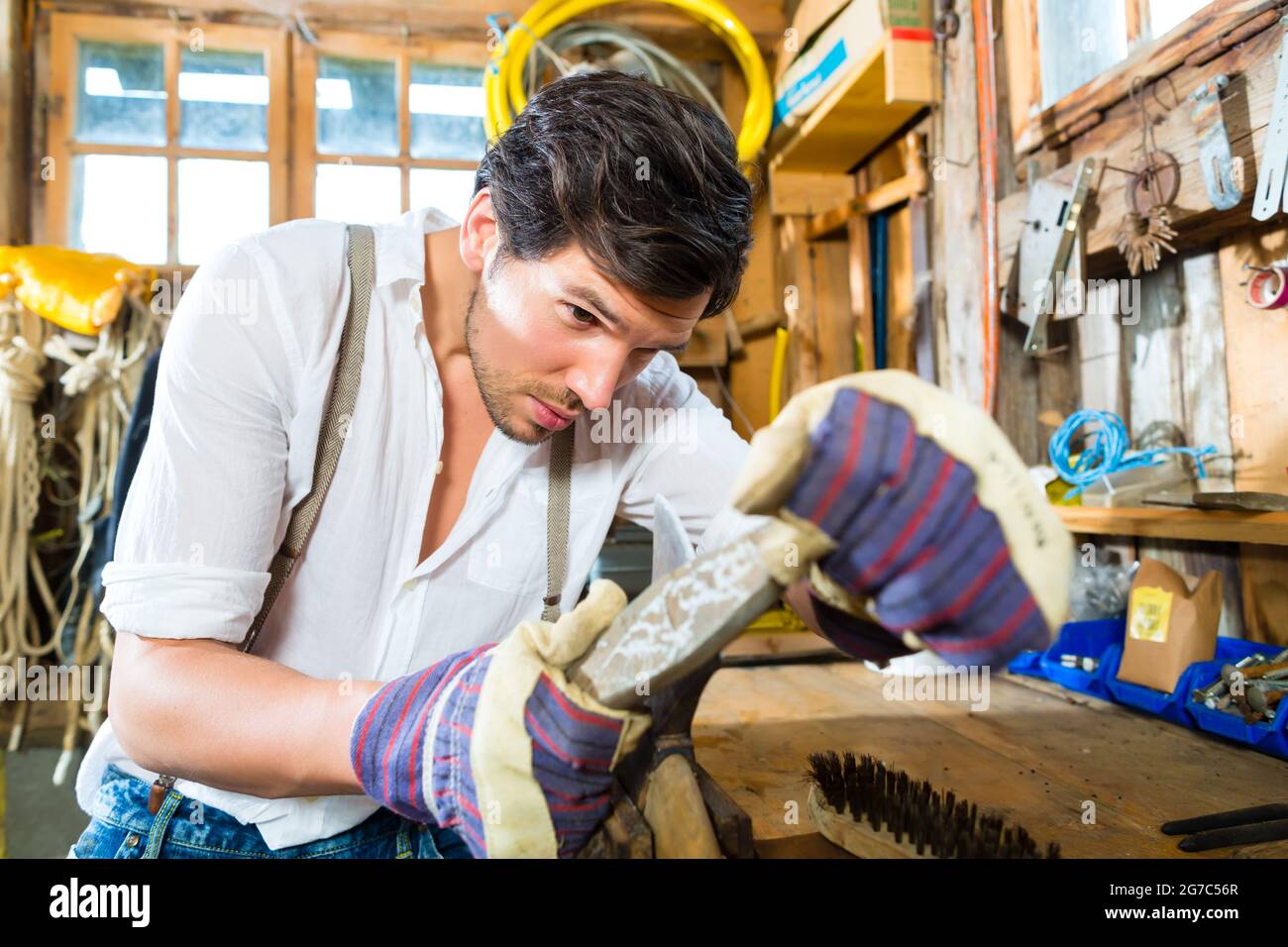 Young man in the Bavarian mountains grinds his axe and sharpening tools ...