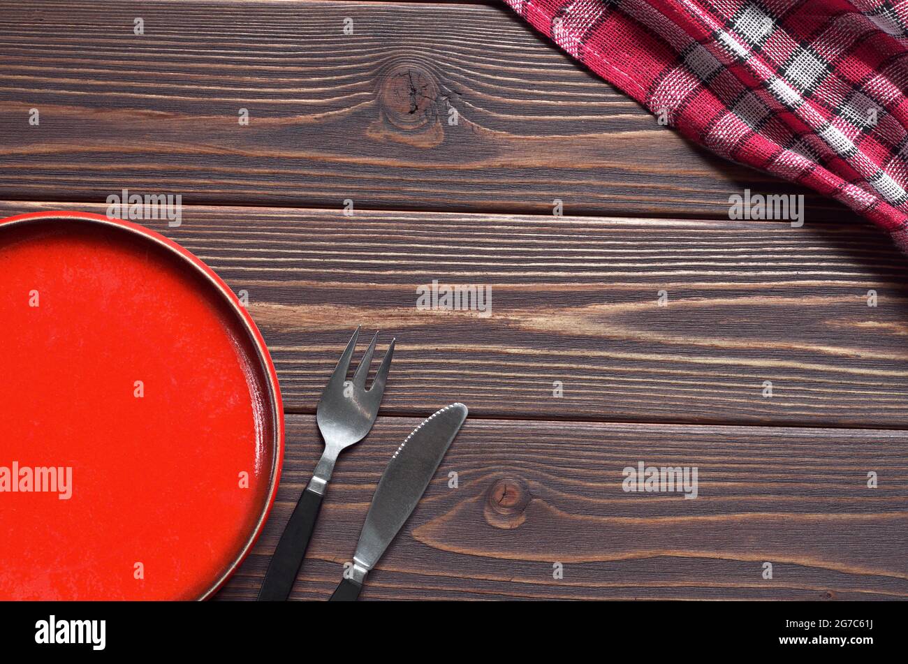 Empty red plate and cutlery on brown wooden table, top view. Space for ...