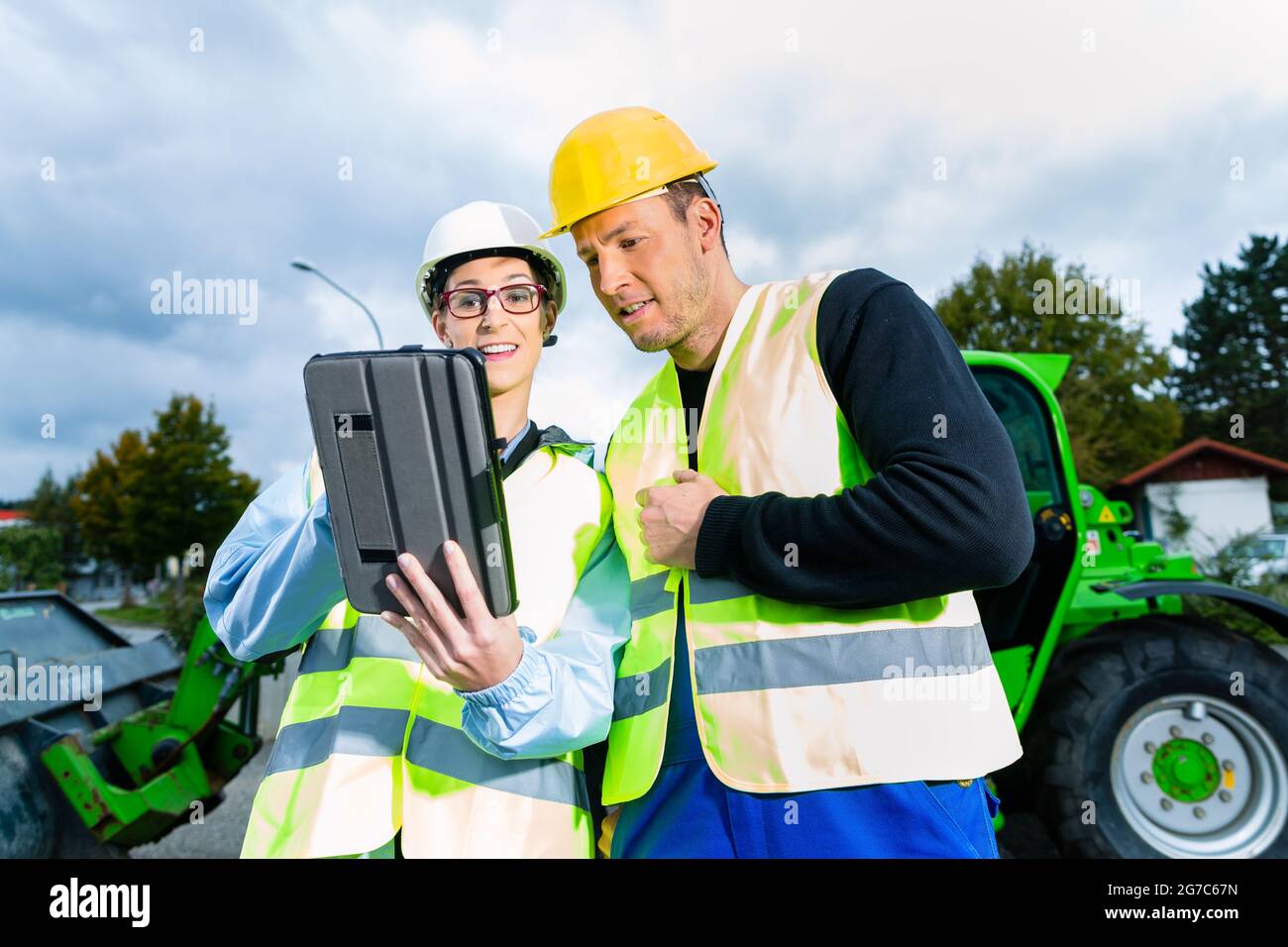 Construction worker and engineer on site discussing blueprints on pad ...