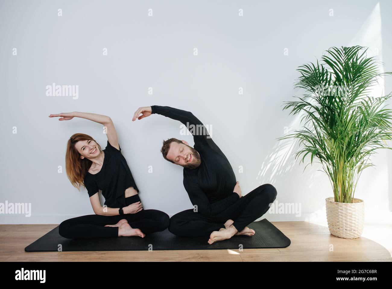 Joyous couple stretching next to each other, sitting on a single mat ...