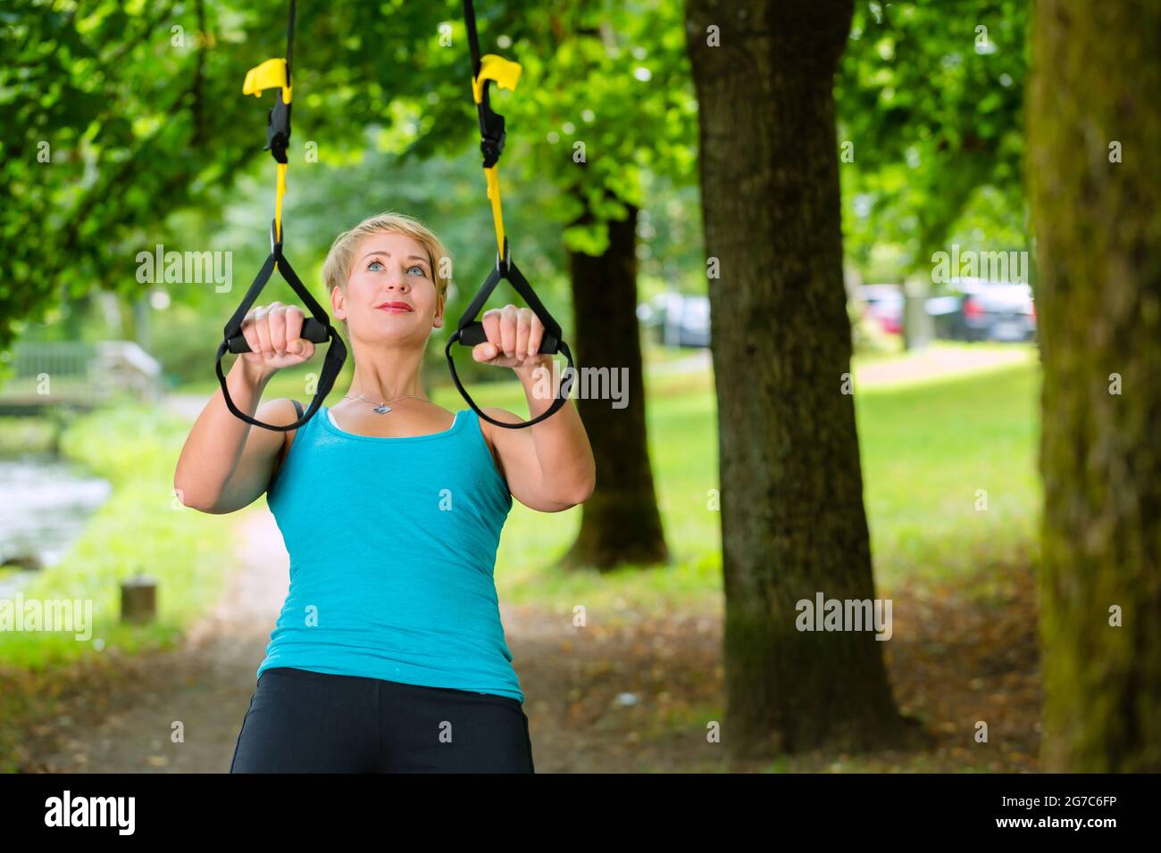 Young woman exercising with suspension trainer sling in City Park under ...