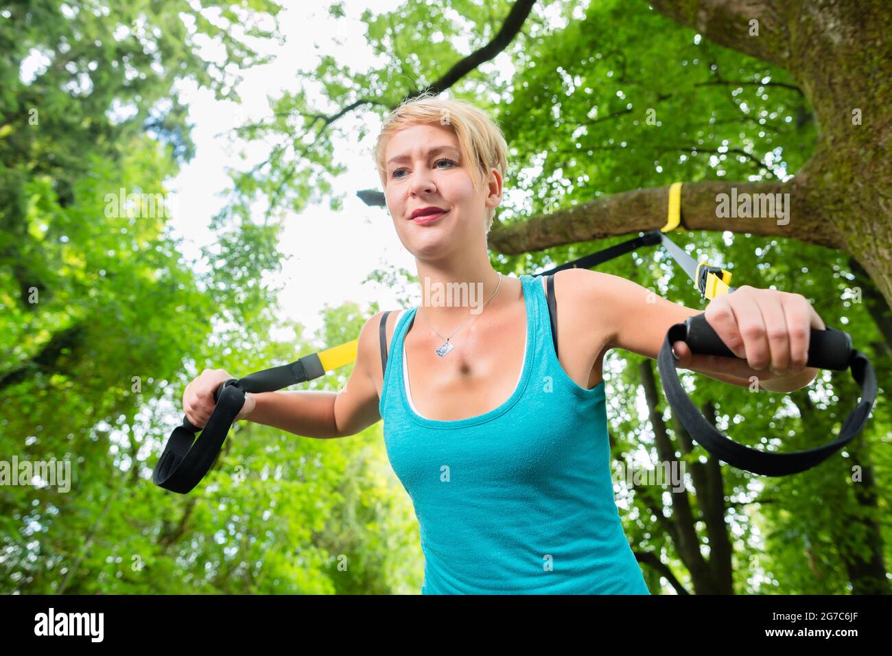 Young woman exercising with suspension trainer sling in City Park under ...