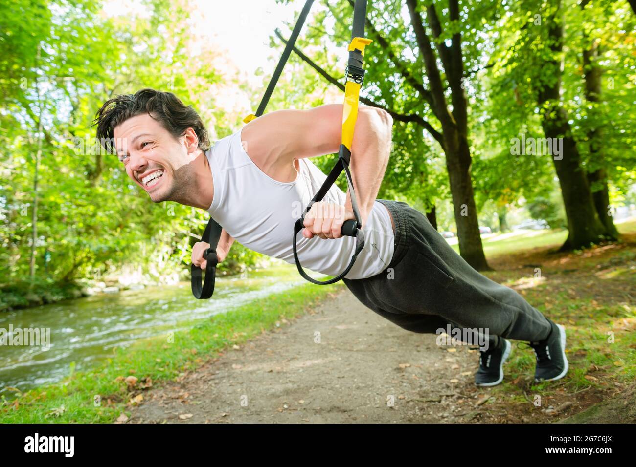 man exercising with suspension trainer sling in City Park under summer ...